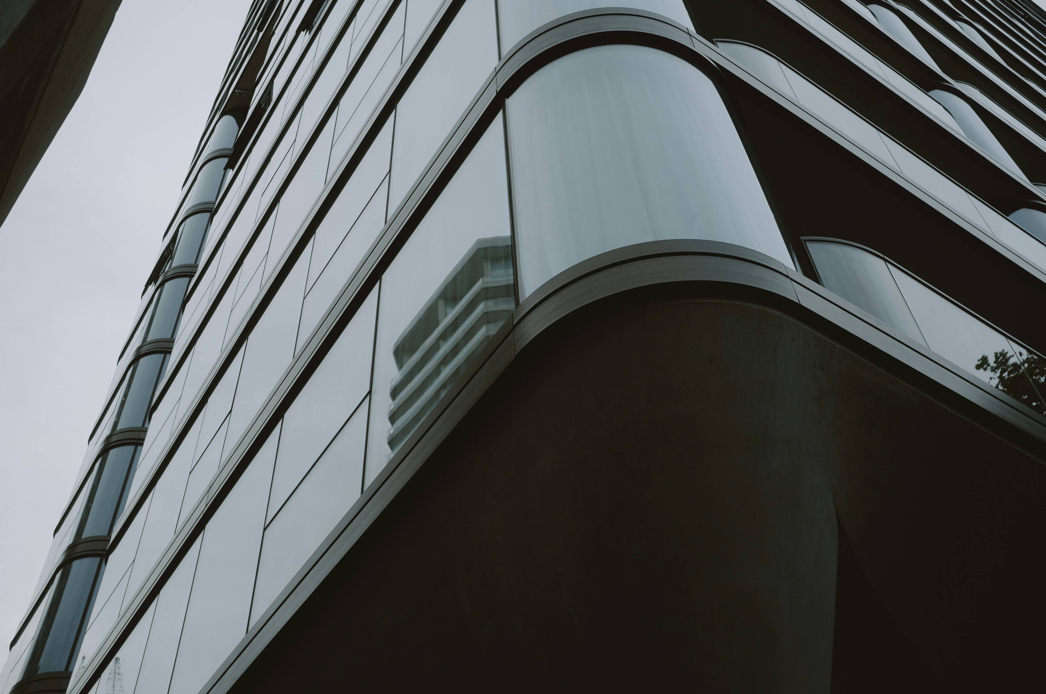 Modern high-rise building with curved glass facade under a cloudy sky.