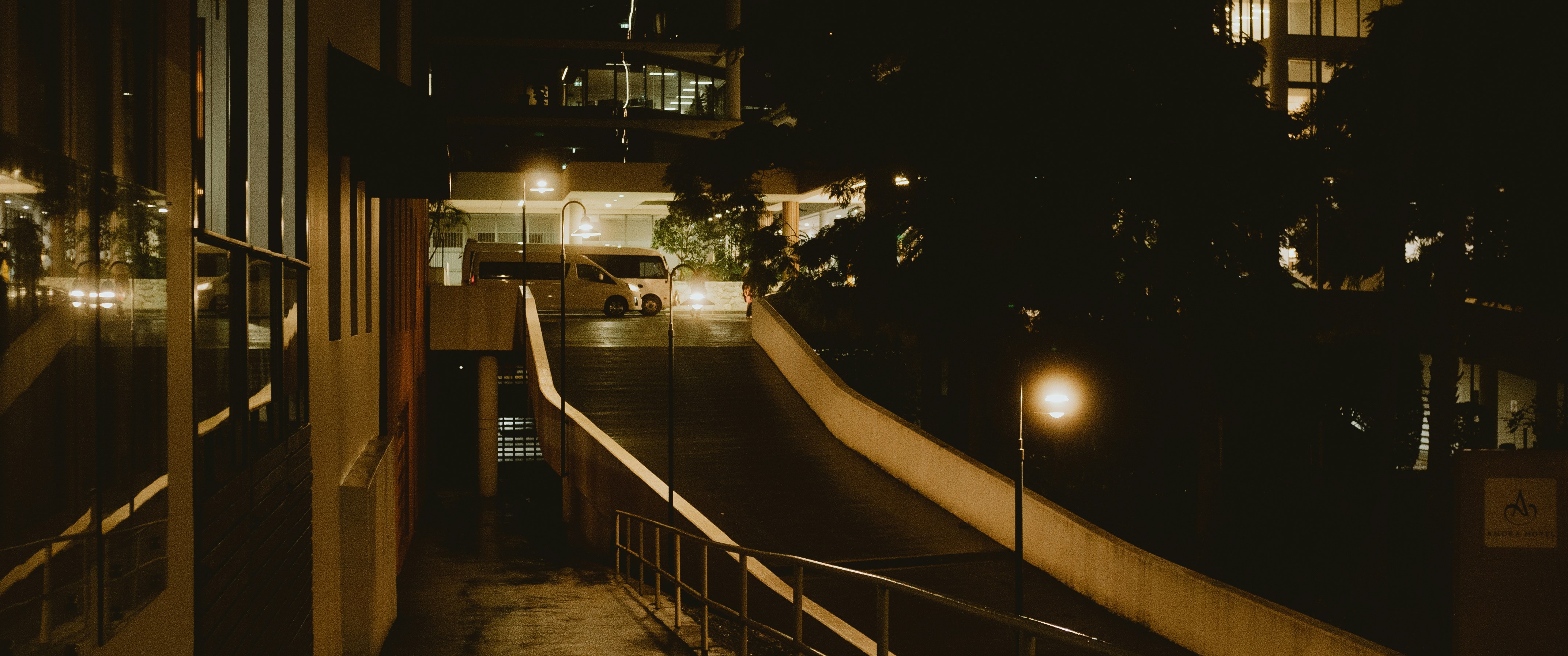 Dimly lit urban path with glowing streetlights and shadowy buildings at night.