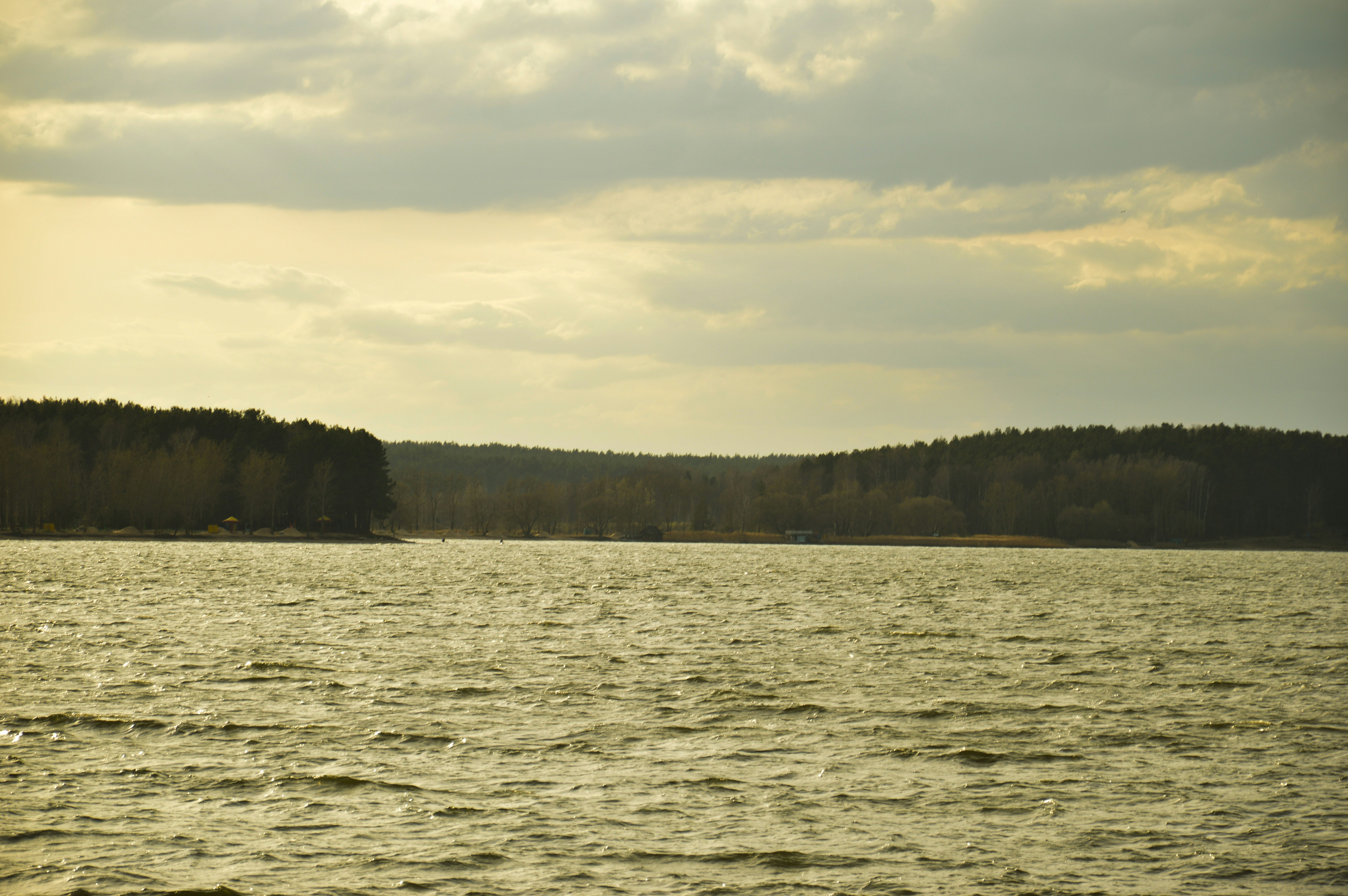 Calm lake under a cloudy sky with distant forested shoreline.
