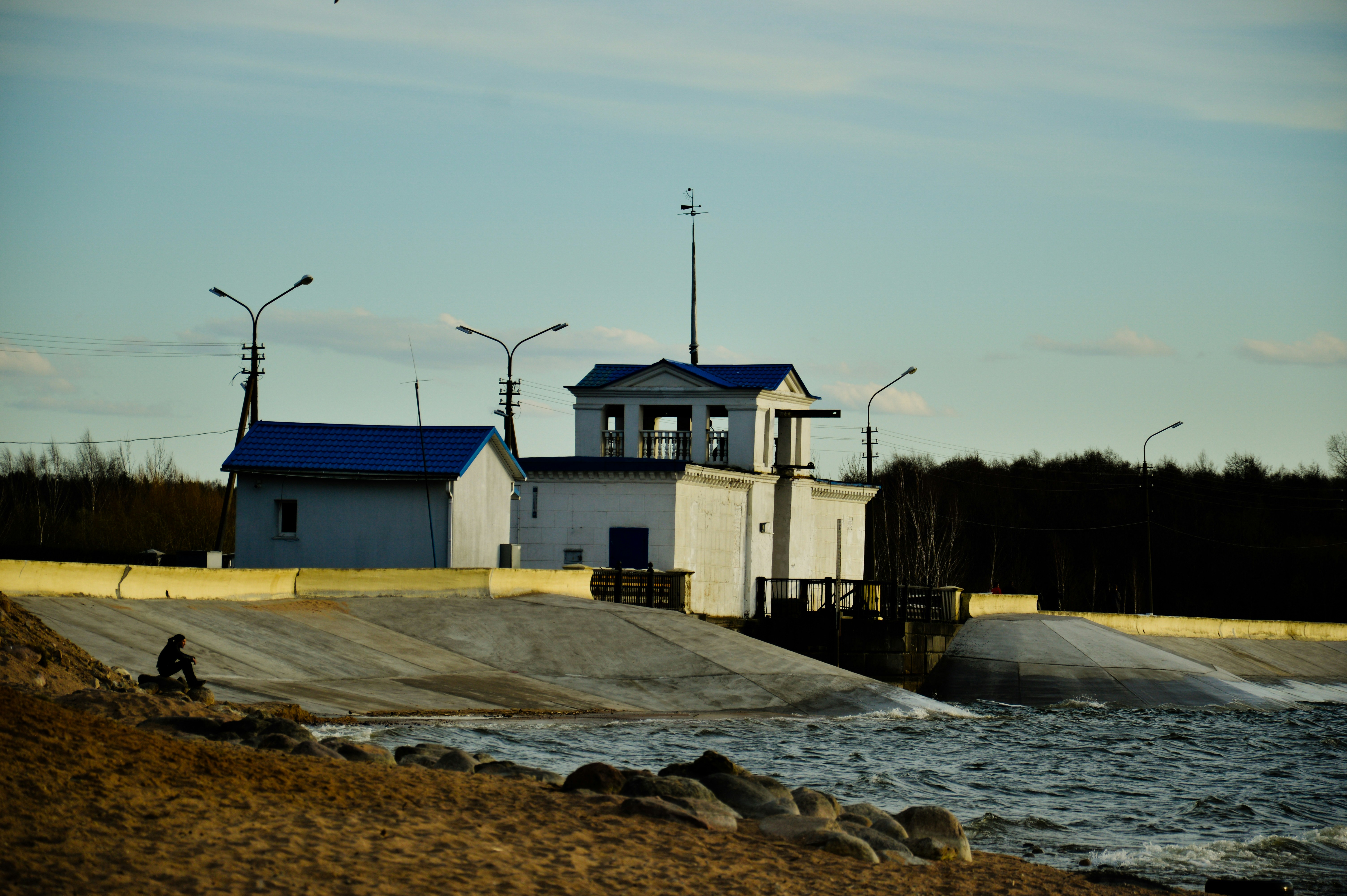 White building with blue roofs near a riverbank, set against a twilight sky.