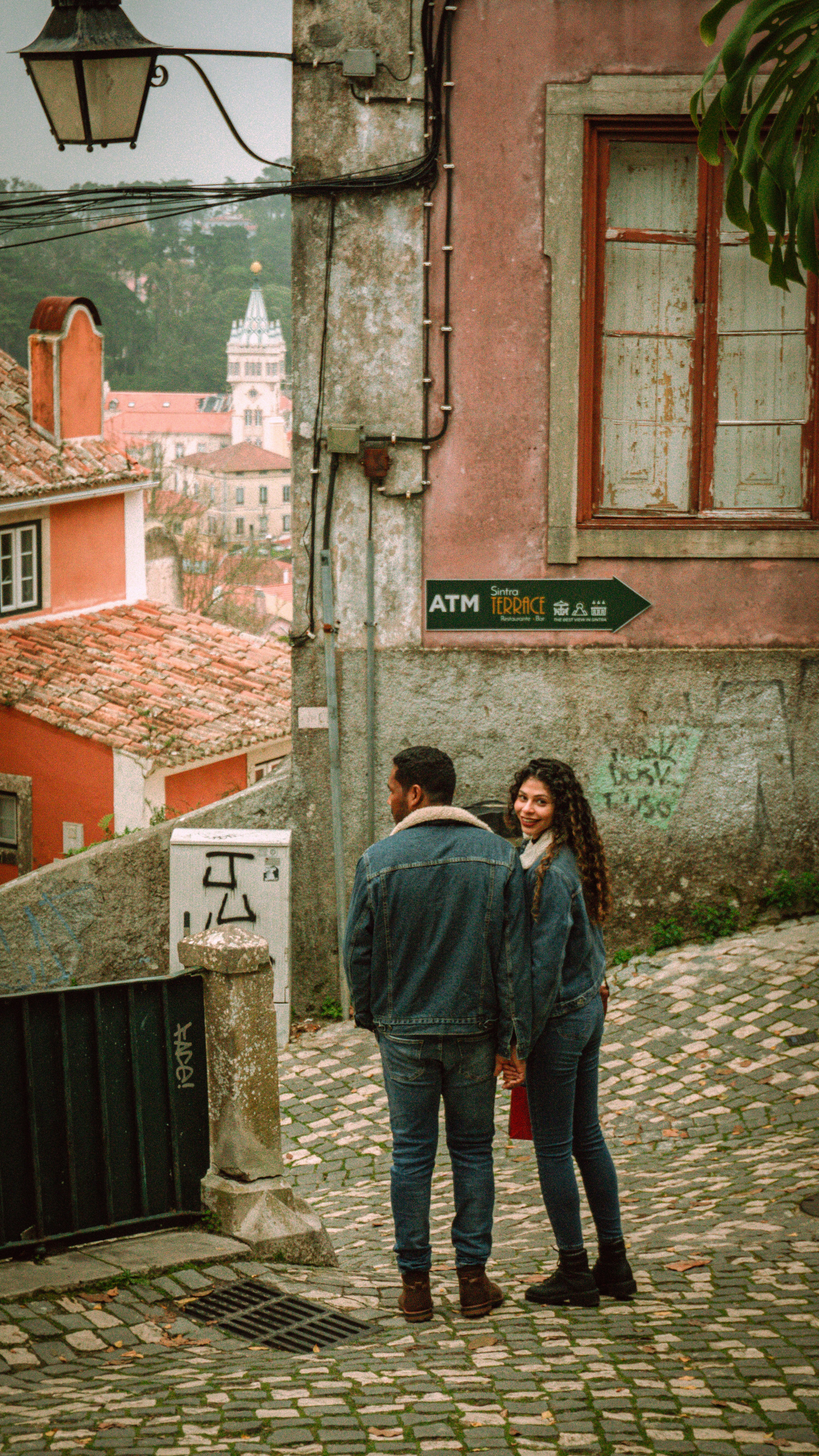 Couple standing on a cobblestone street in a historic town with colorful buildings and distant church tower.