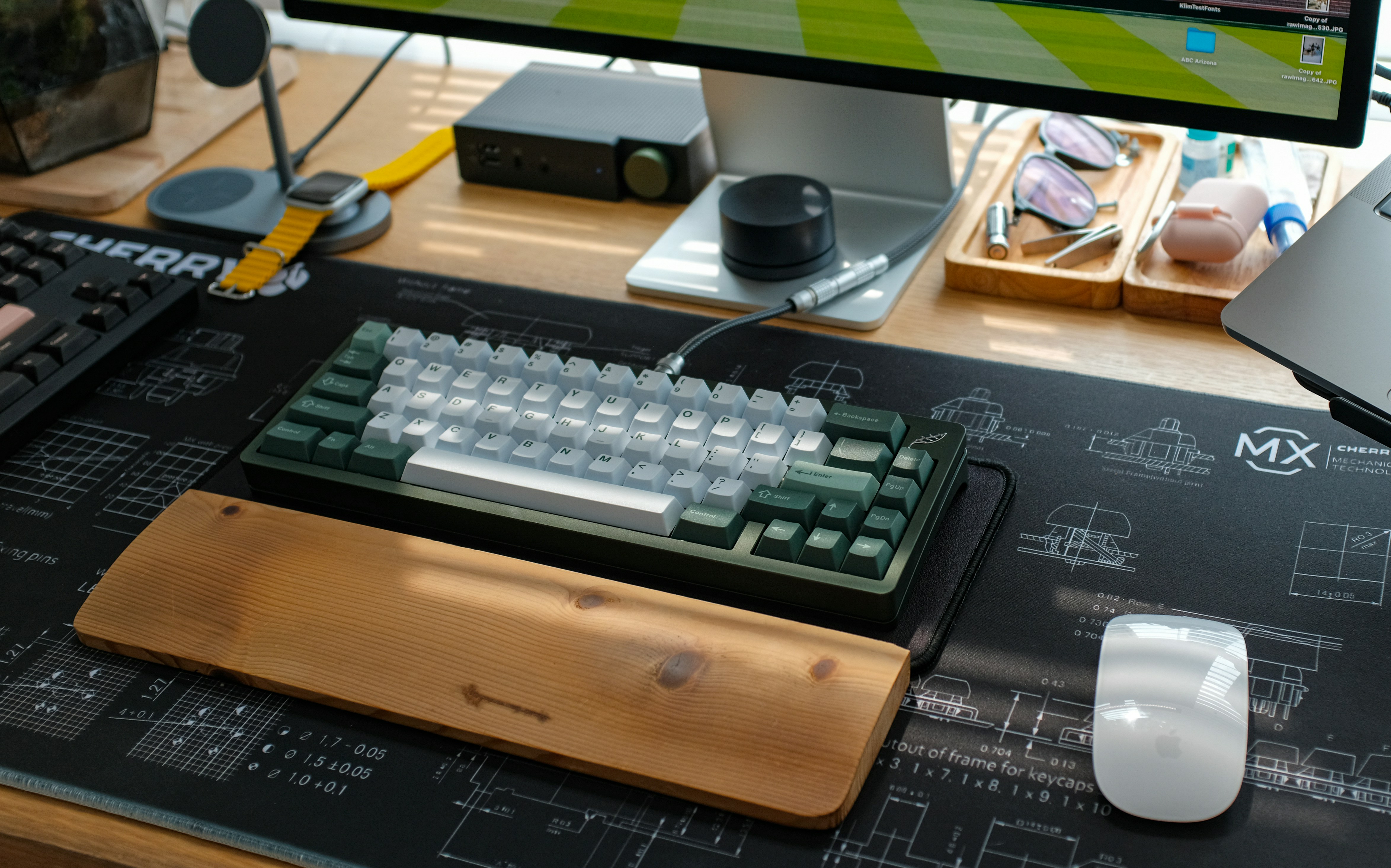 Mechanical keyboard with a green and white color scheme on a detailed blueprint mouse pad, accompanied by a sleek mouse and various desk accessories.