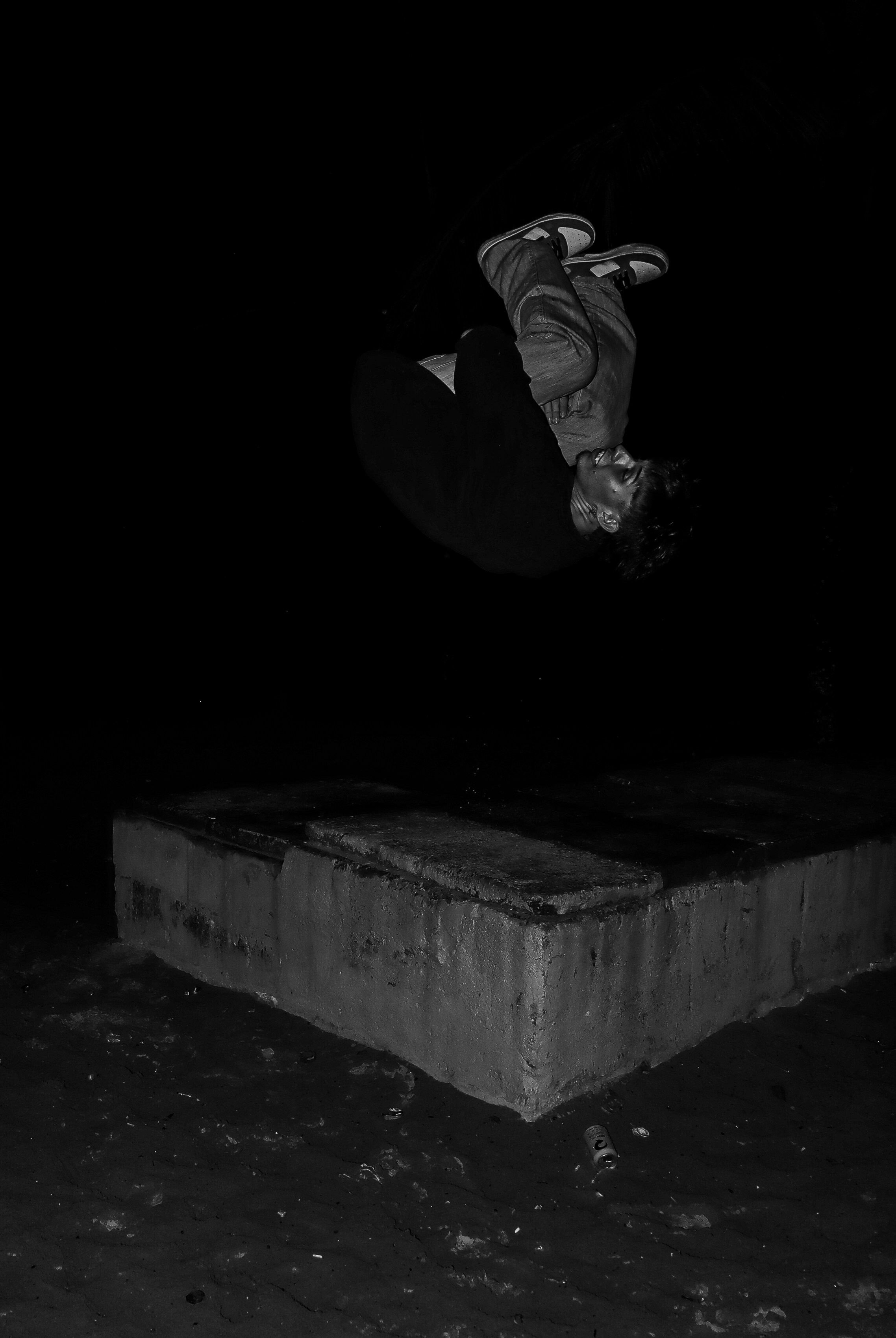Person performing a somersault over a concrete block in darkness.