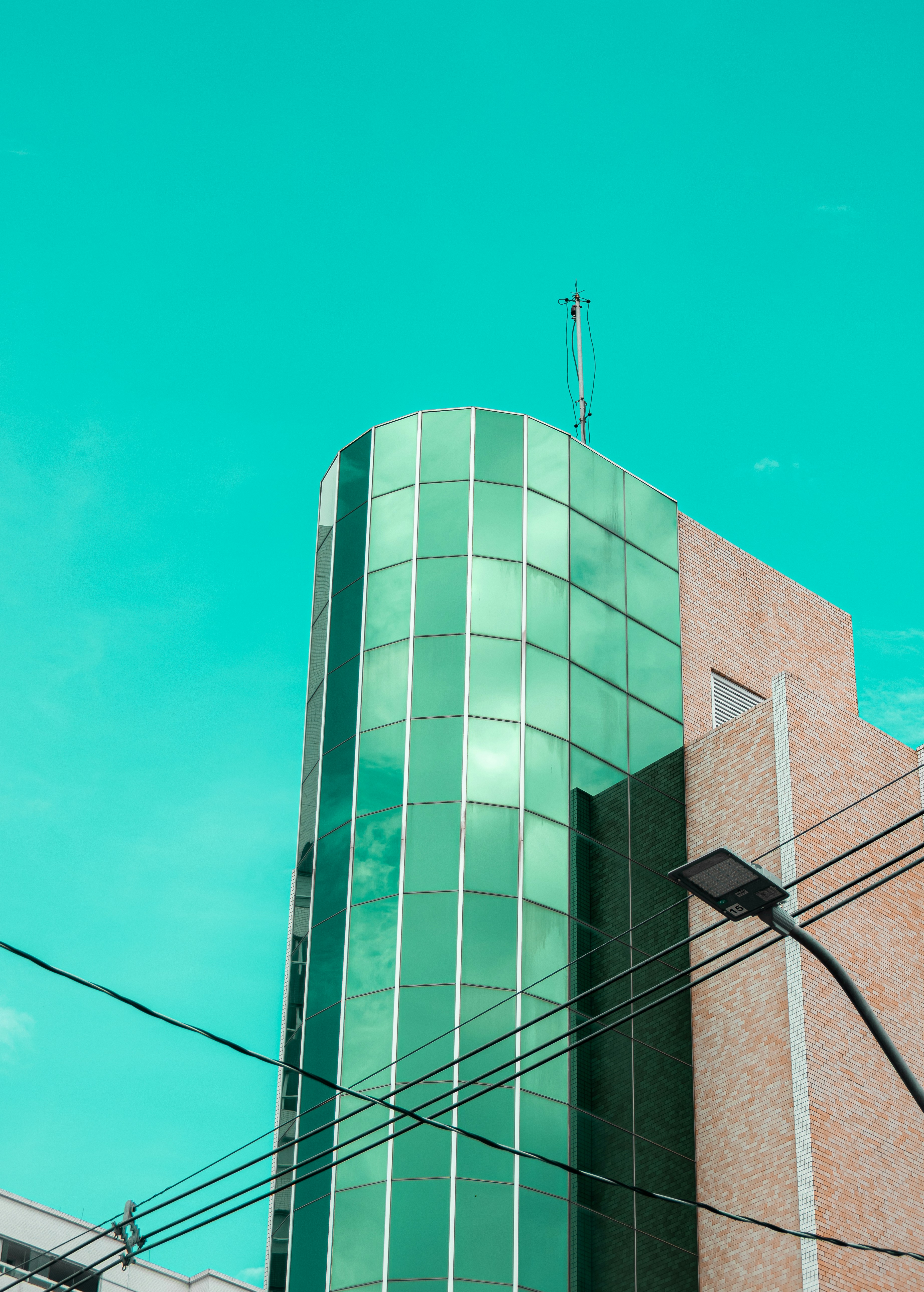 A contemporary building with a curved glass facade reflecting the sky, intertwined with power lines in the foreground.
