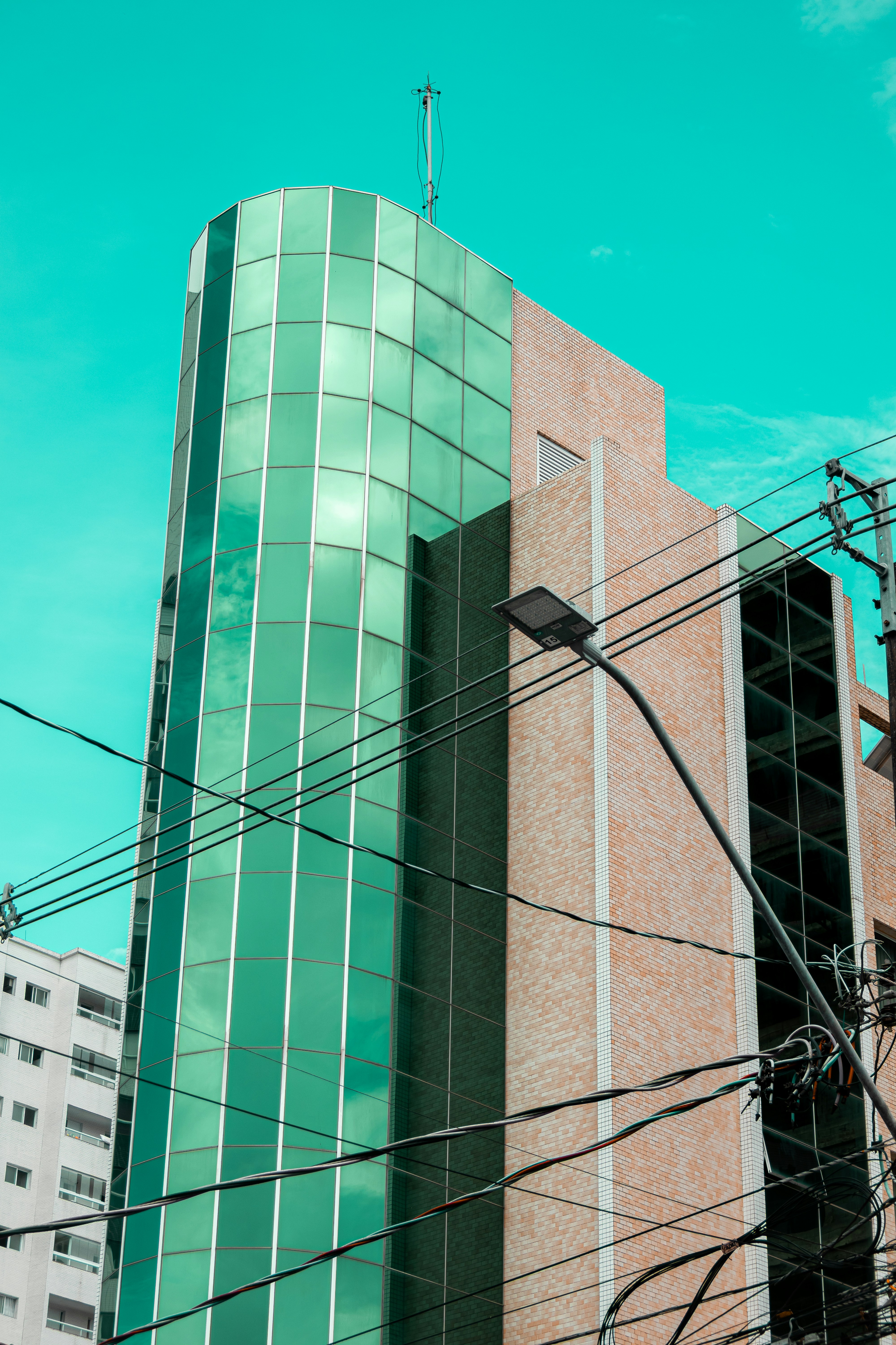 Modern building with green-tinted glass facade and intersecting power lines against a clear sky.