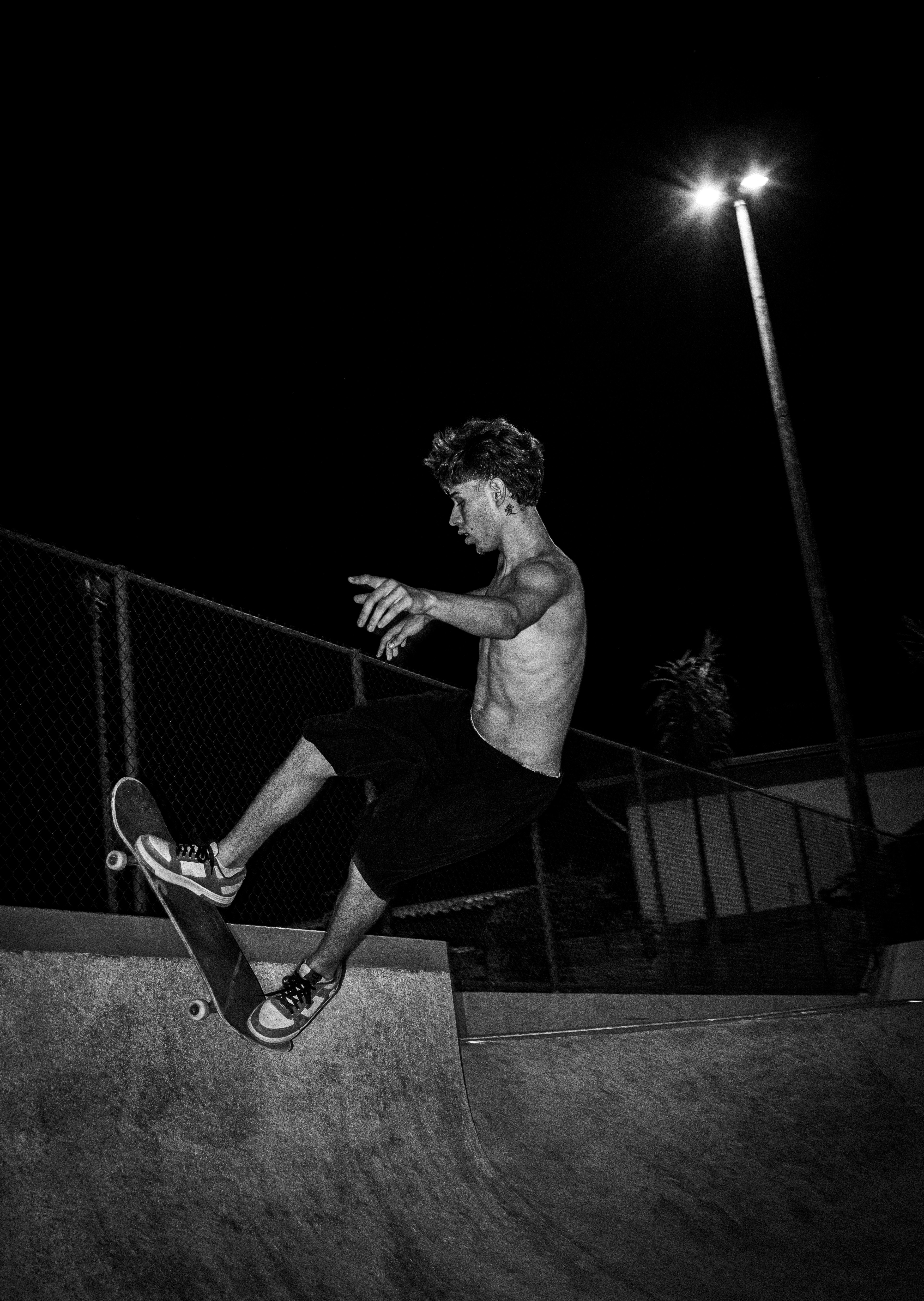 Skateboarder executing a trick under bright streetlights at night.