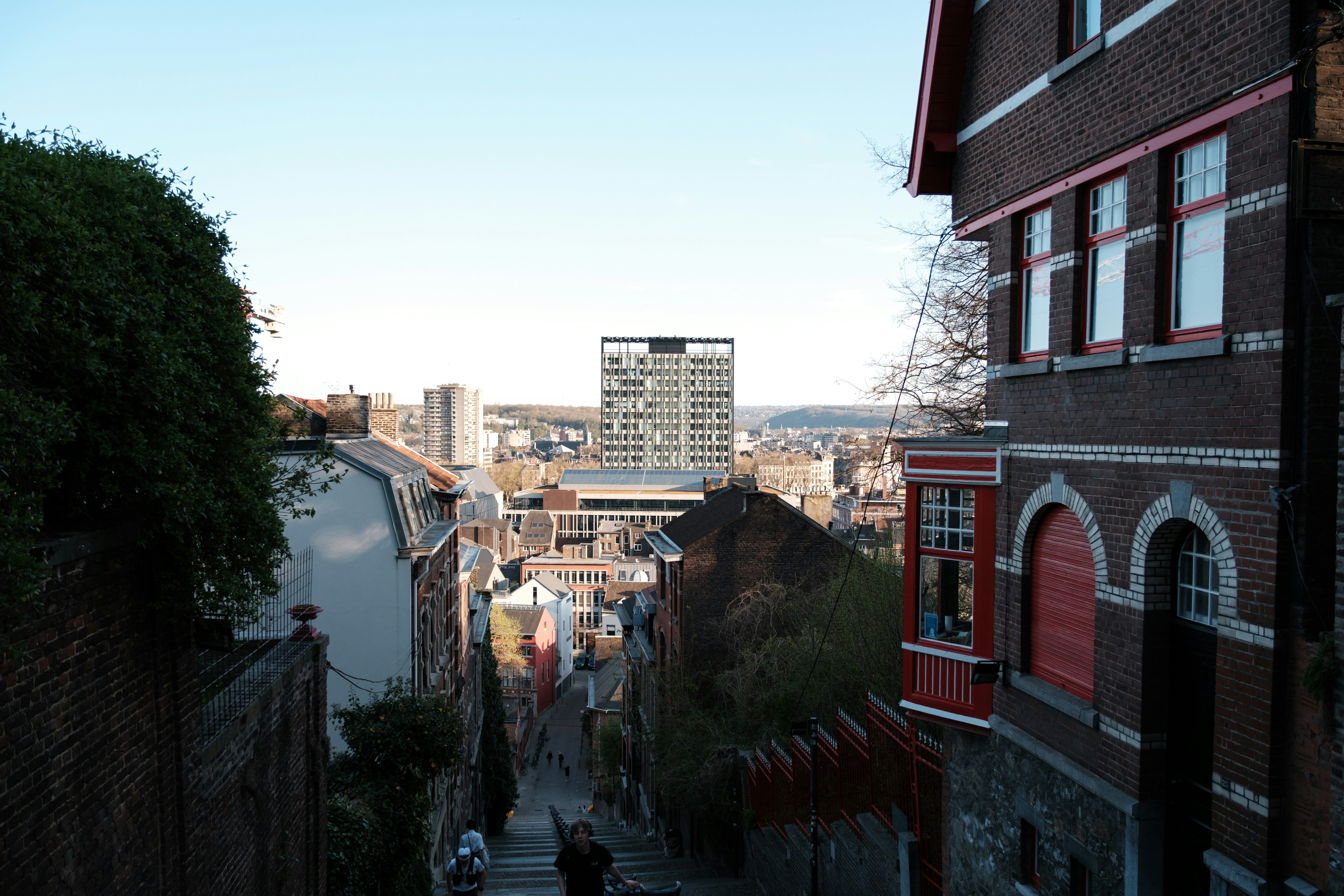 Narrow alleyway leading down to a cityscape with a distant modern building under a clear blue sky.