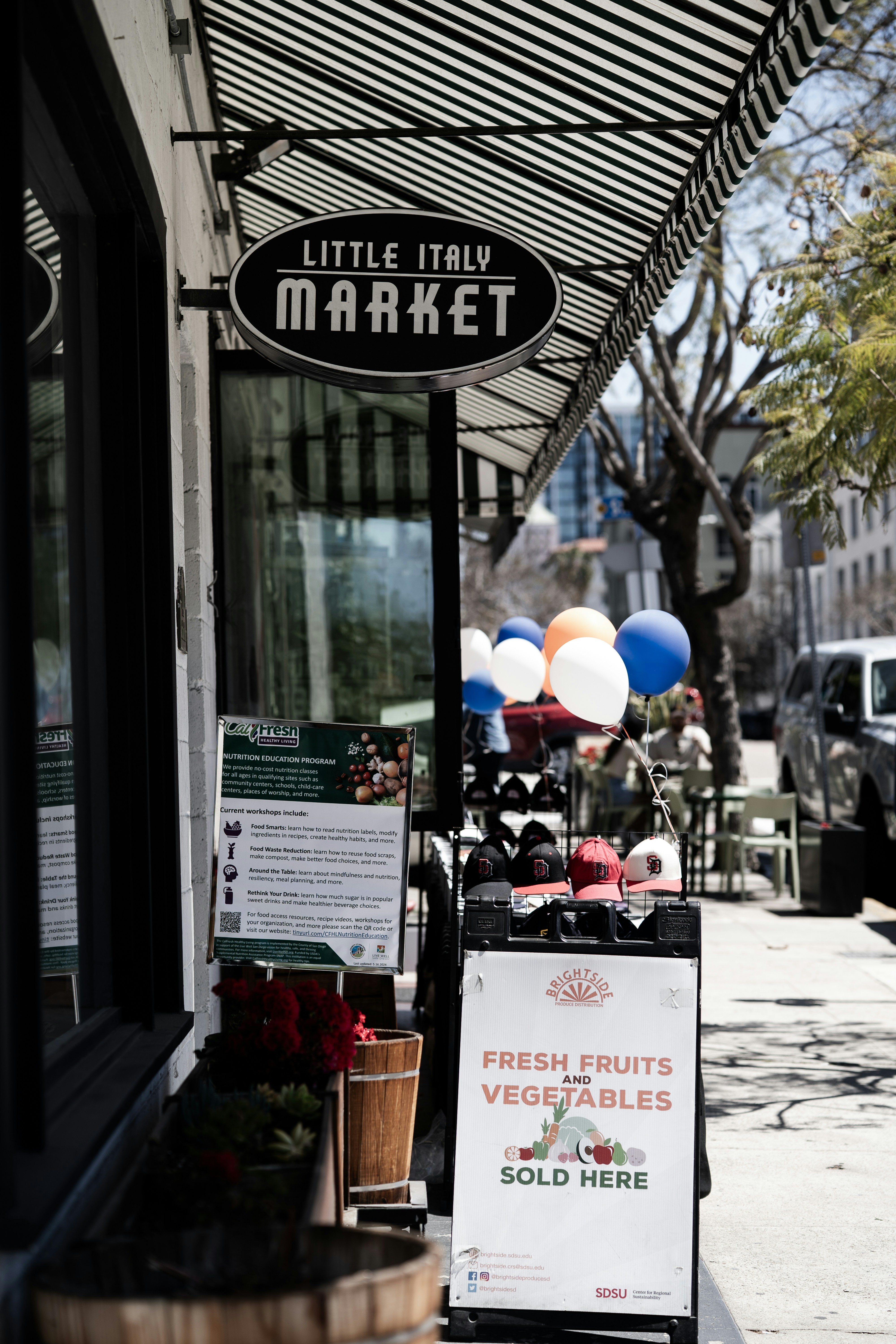 Under the Striped Canopy: Little Italy Market Sign and Fresh Produce Board