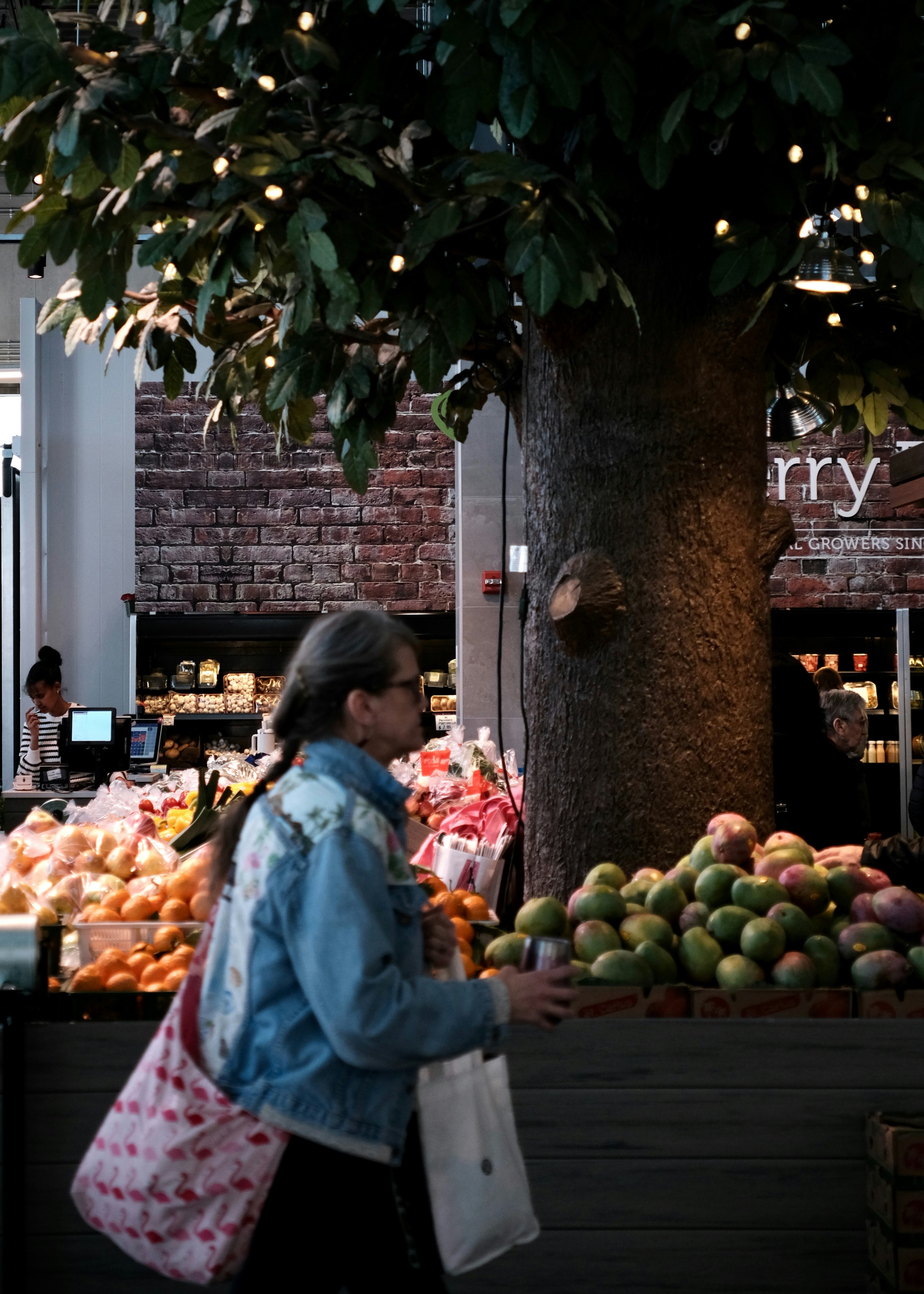 Under the Market Canopy: Denim-Clad Shopper Among Fresh Fruit