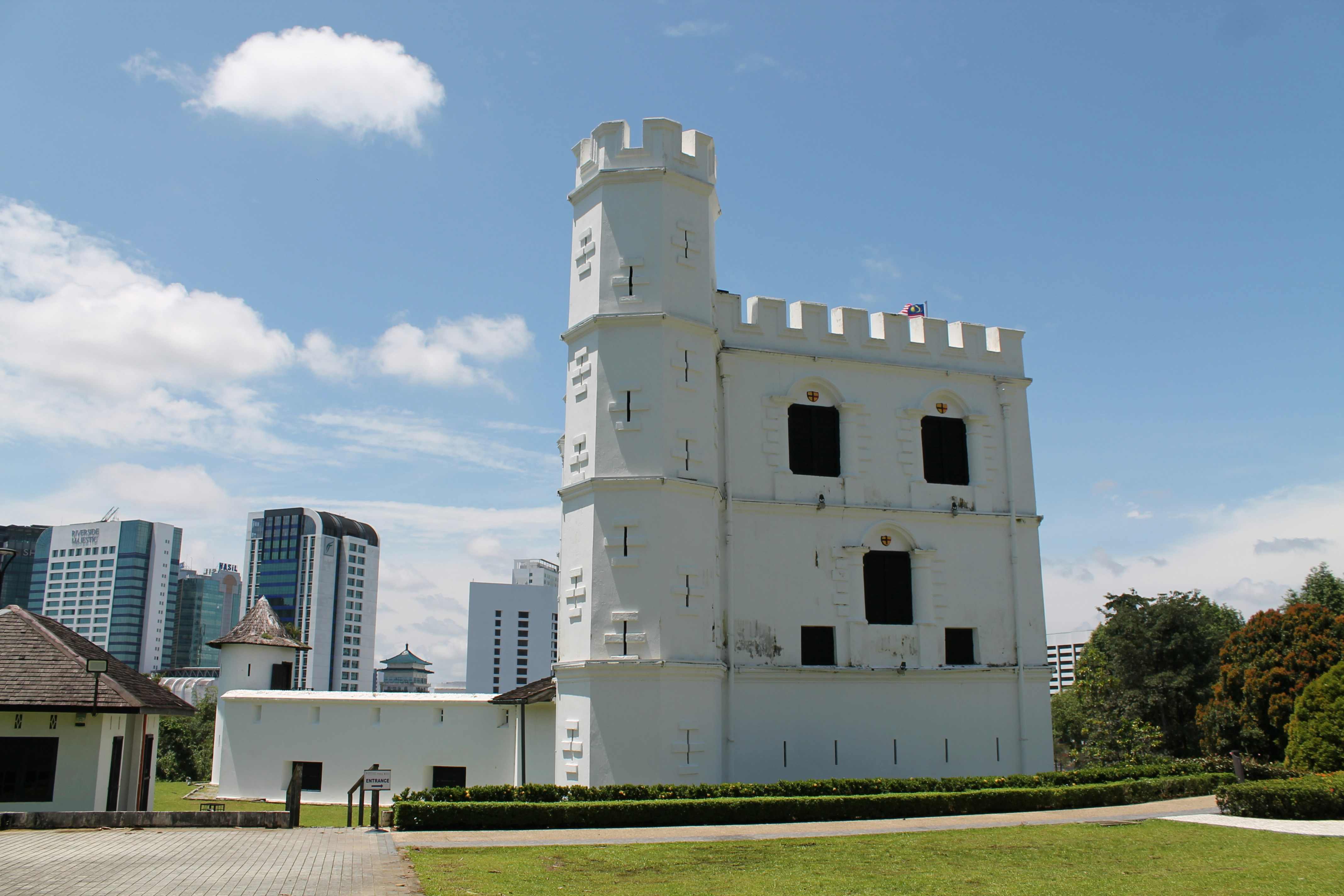 White historic tower with crenellations against a backdrop of modern skyscrapers under a clear blue sky.