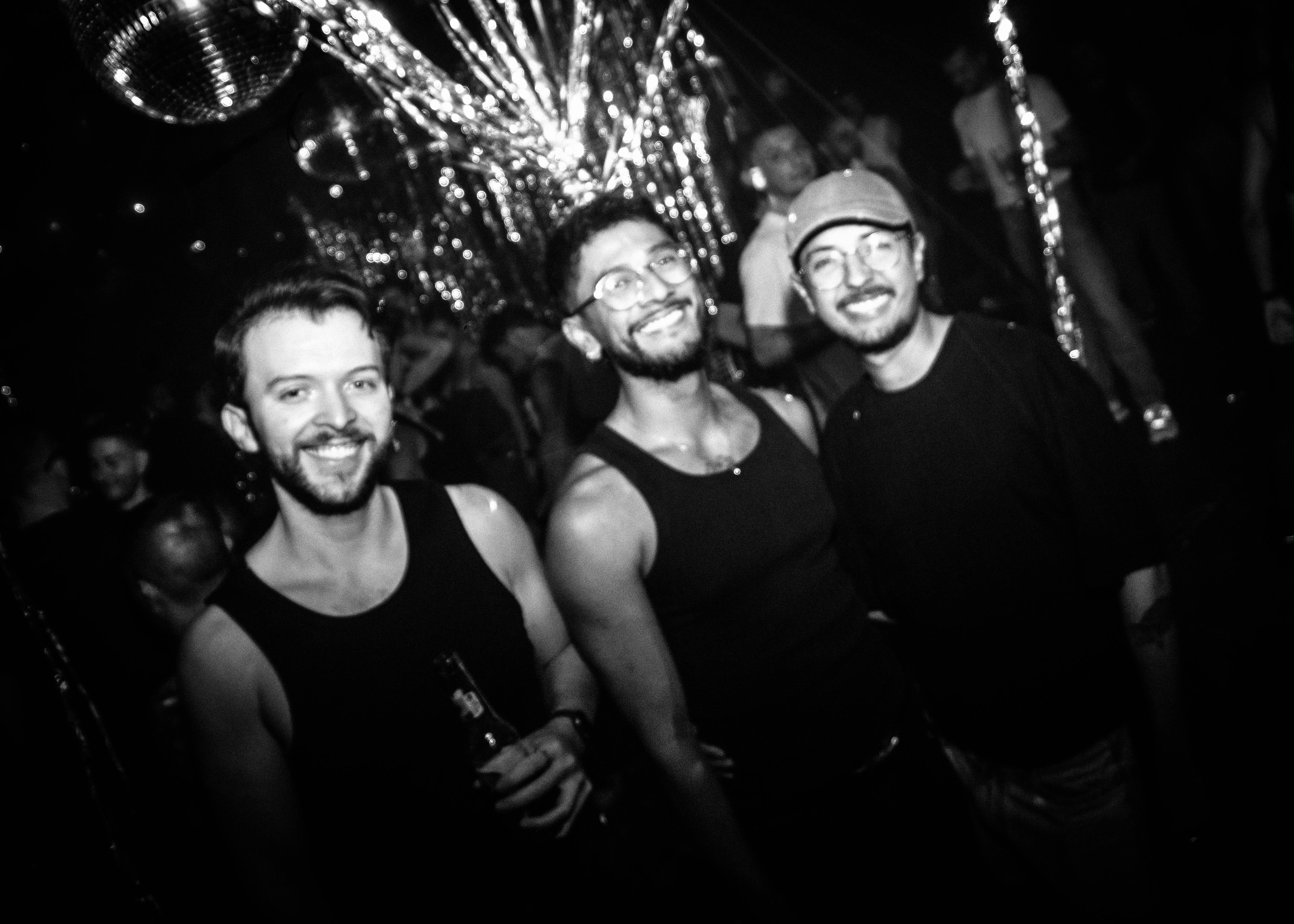 Three people smiling in a dimly lit club with sparkling lights in the background.