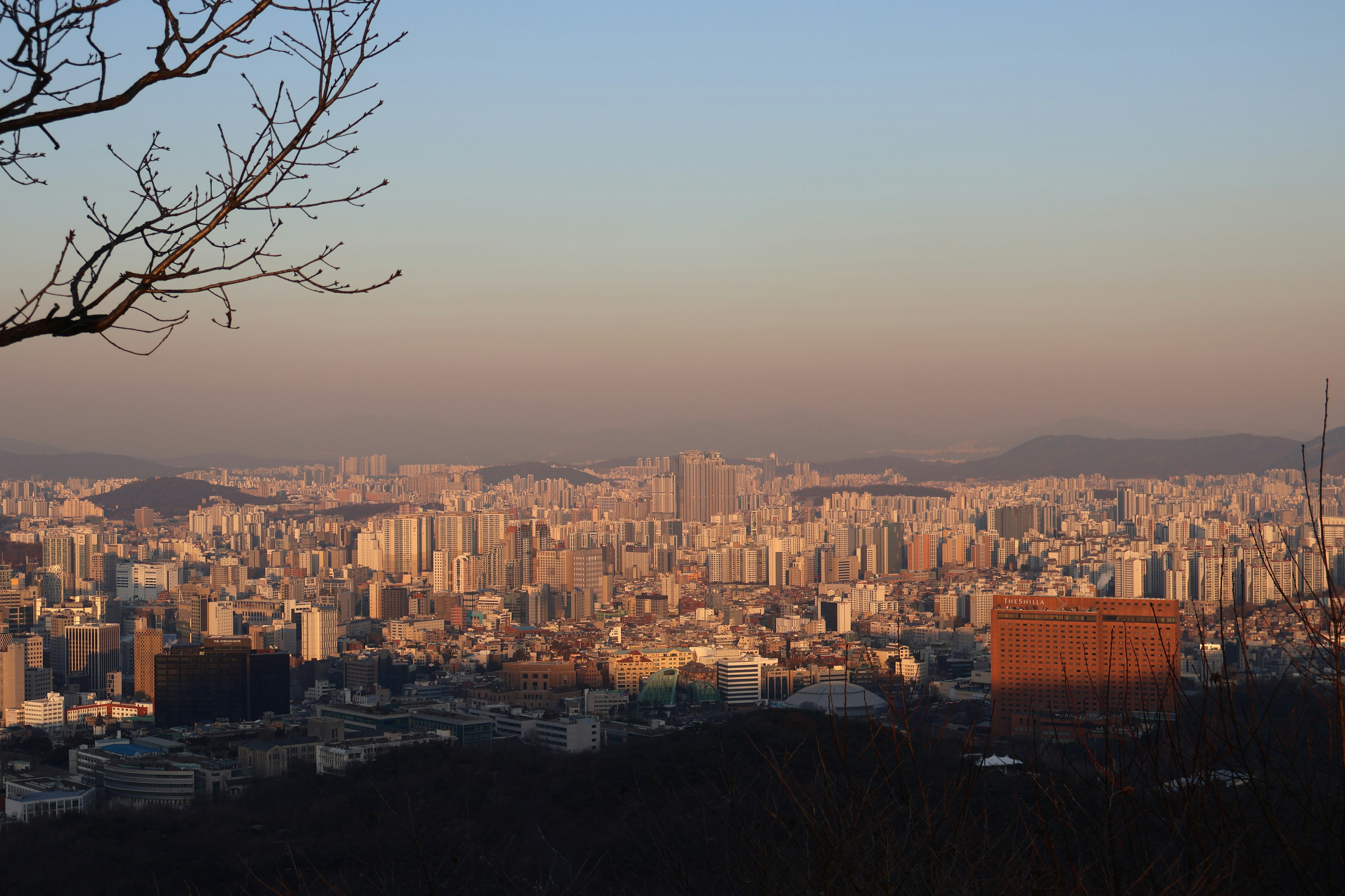 Expansive city skyline bathed in warm sunset light with distant mountains under a clear sky.
