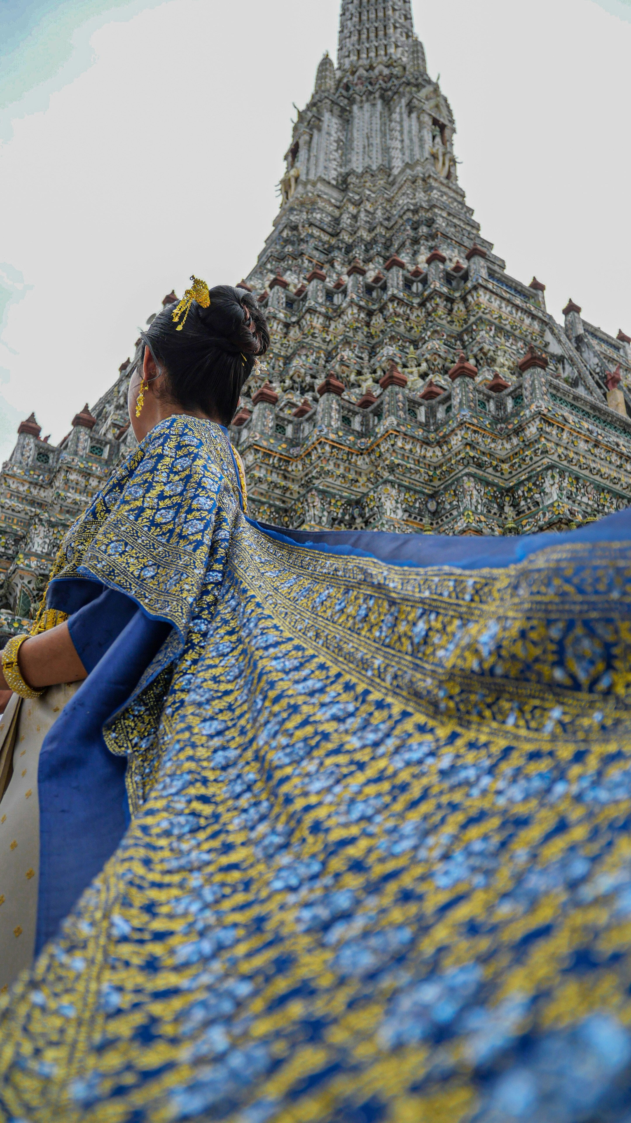 Person in ornate blue and gold attire standing before a towering temple structure.