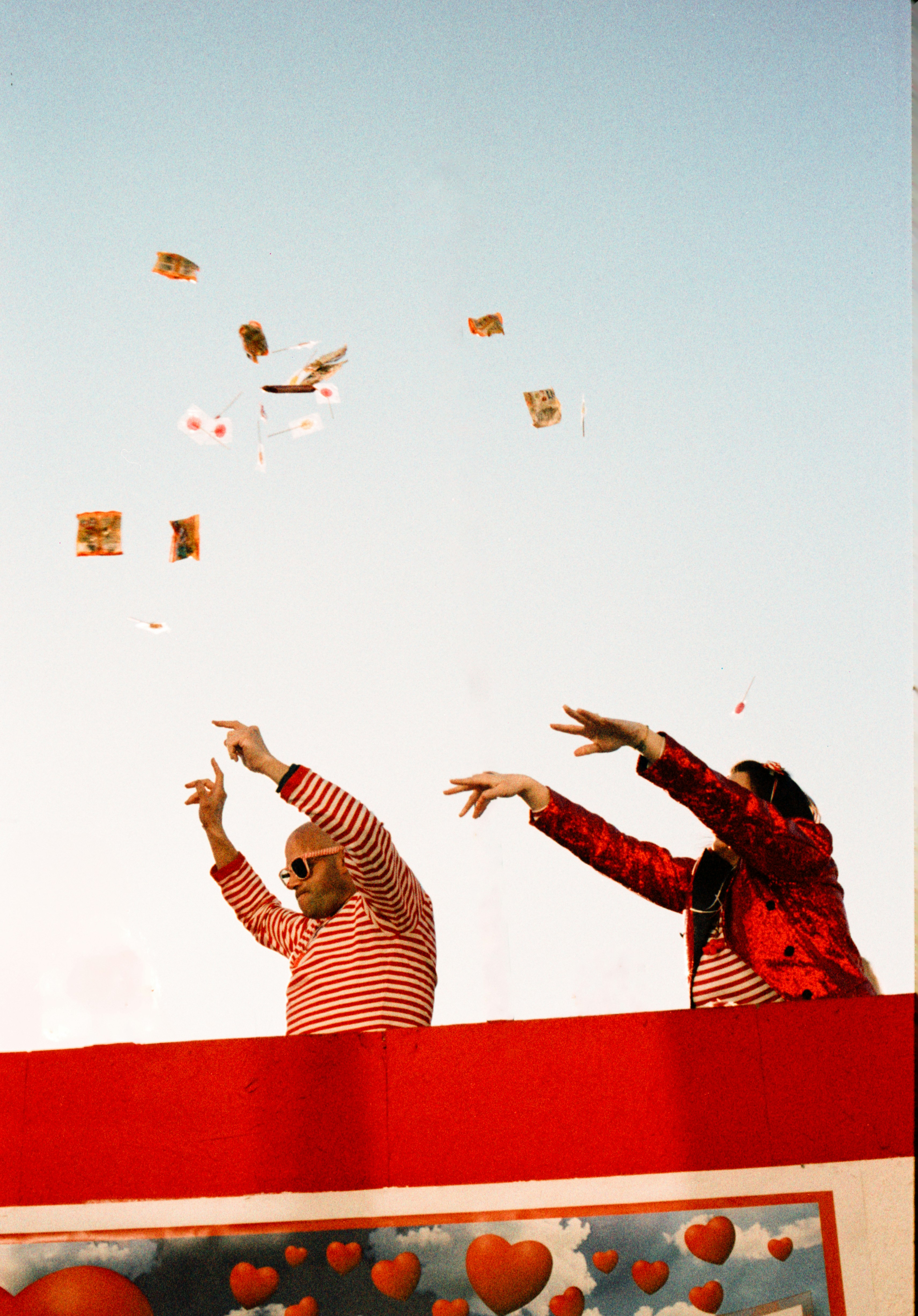 Two costumed participants of Cologne’s famous Rose Monday Parade throw candy from a brightly decorated carnival float into the cheering crowd. With clear skies and vibrant energy, this image captures the joy, tradition, and colorful spirit of Germany’s Rhineland Carnival at its peak.,