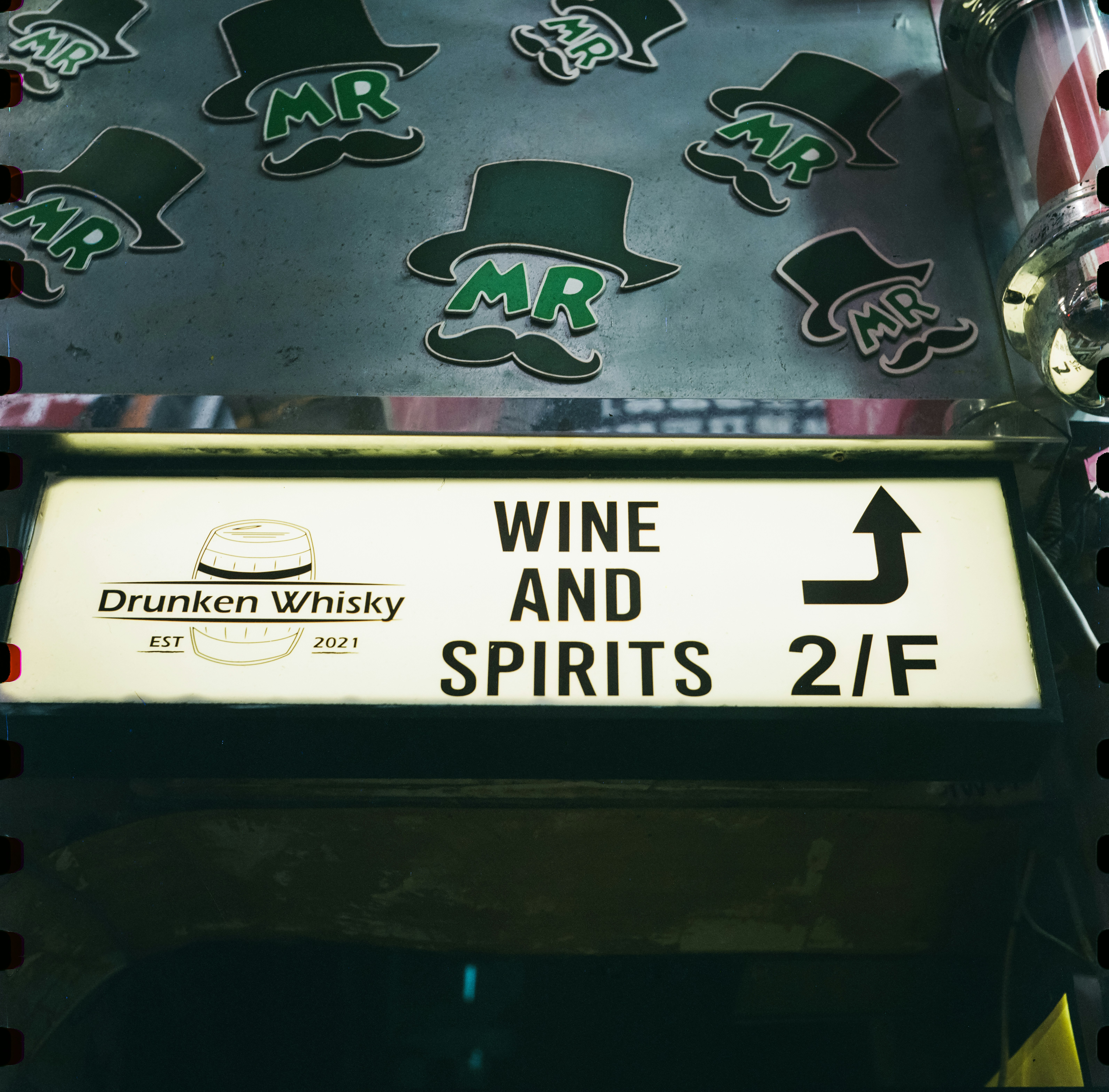 Stickers of top hats and mustaches beside a lightbox sign directing to a wine and spirits shop on the second floor.