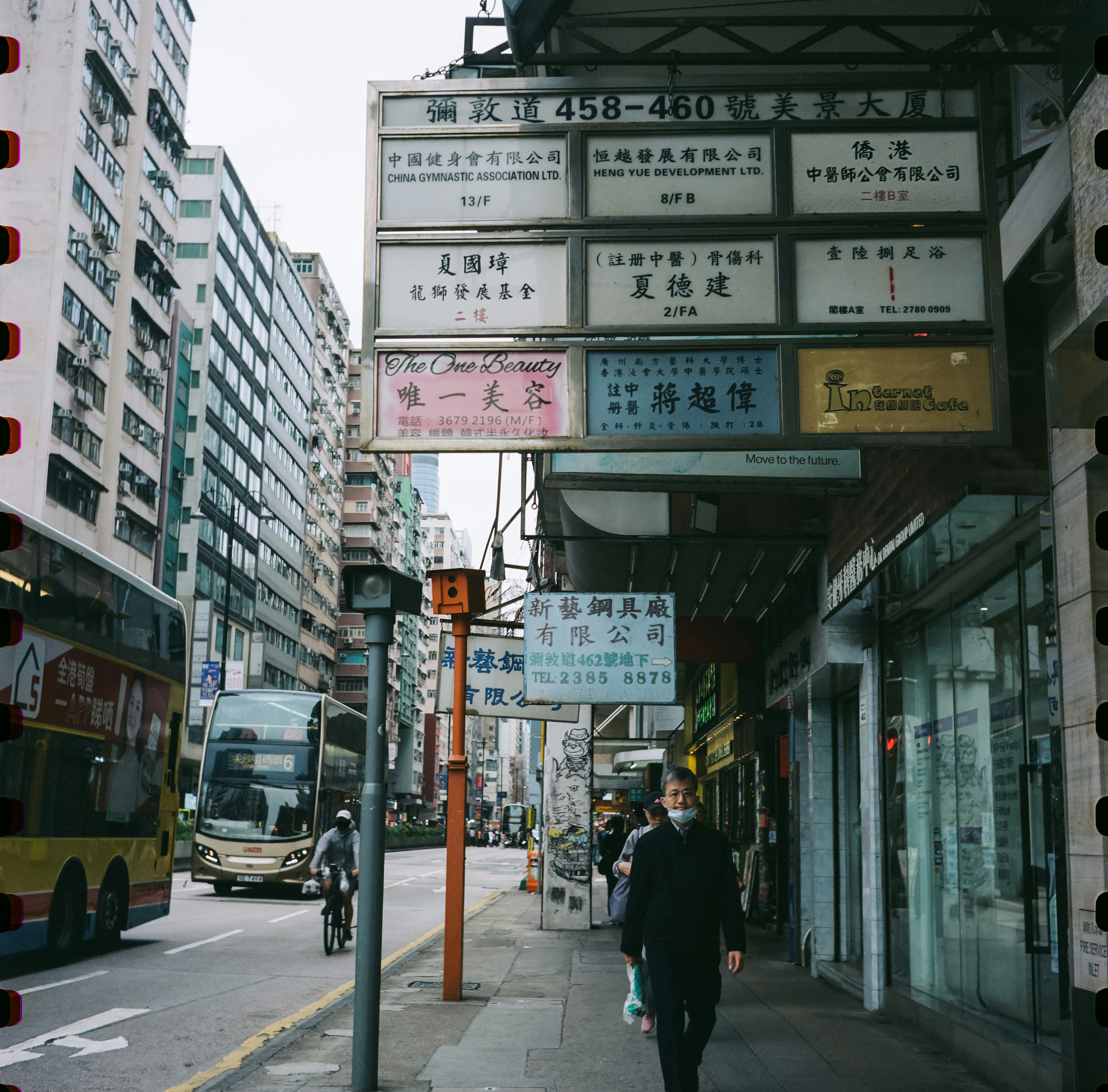 City street lined with numerous overhead signs and bustling with pedestrians and double-decker buses.