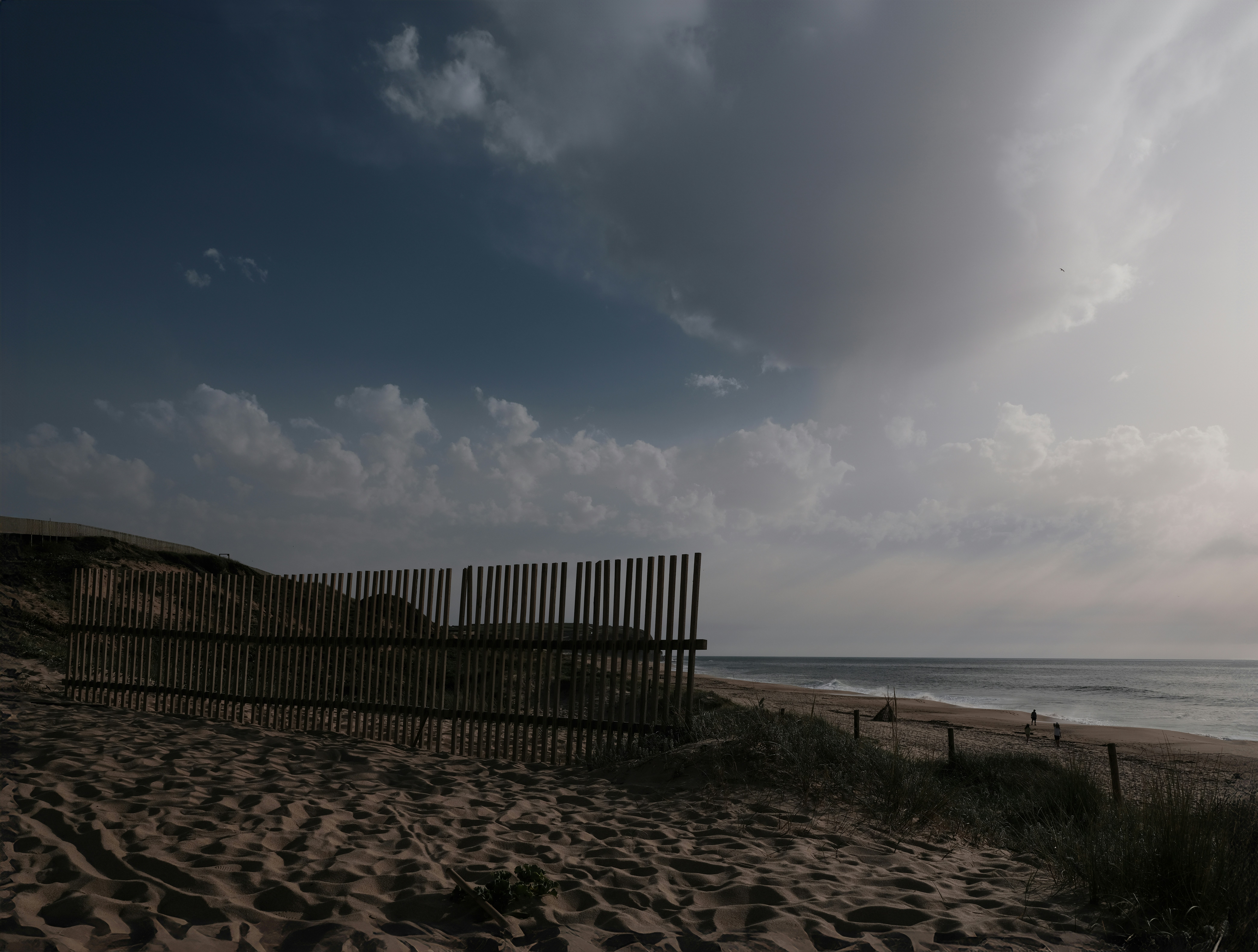 Rustic wooden fence on sandy beach with ocean and dramatic sky in the background.