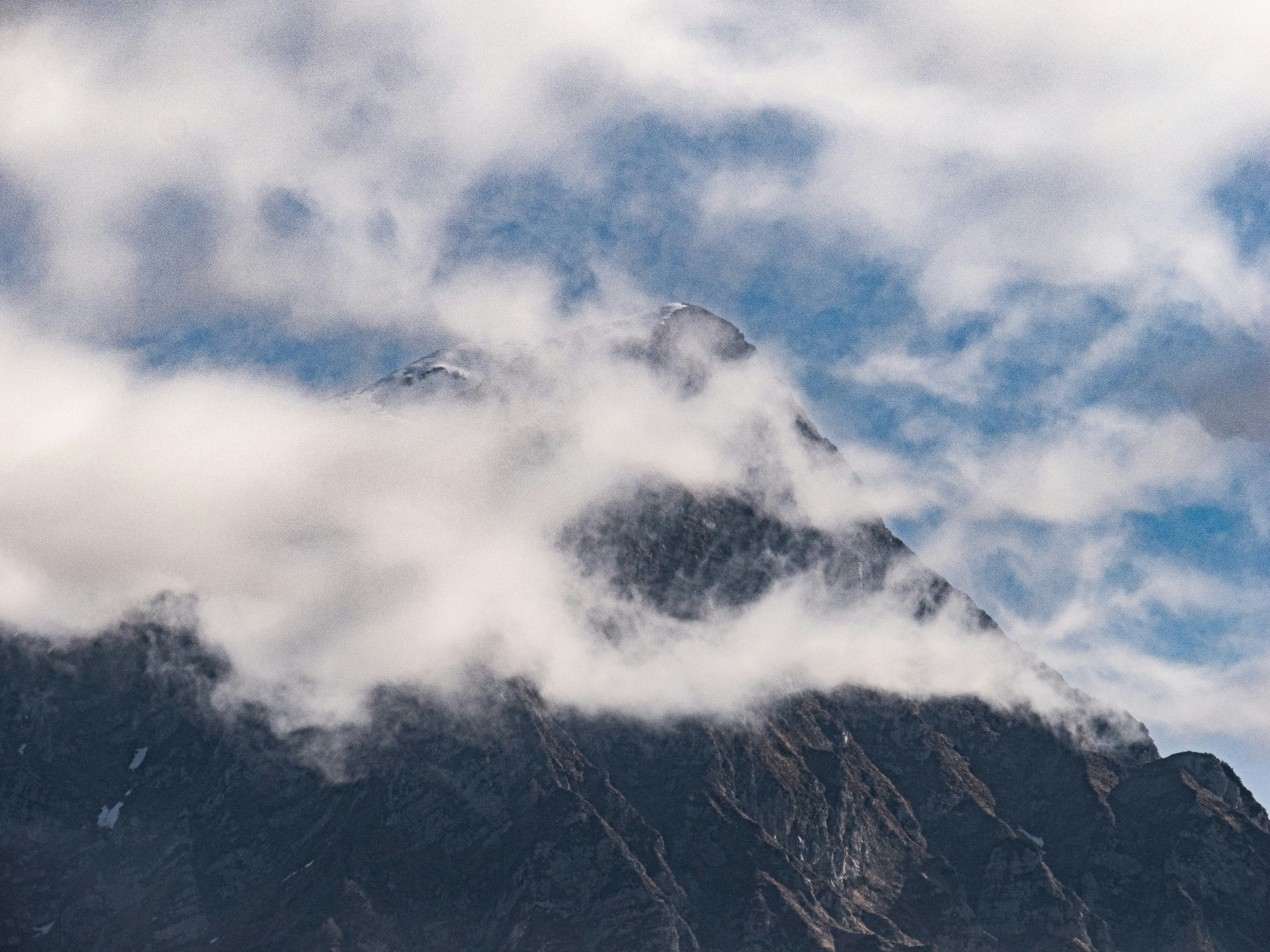Mountain partially obscured by swirling clouds under a bright blue sky.