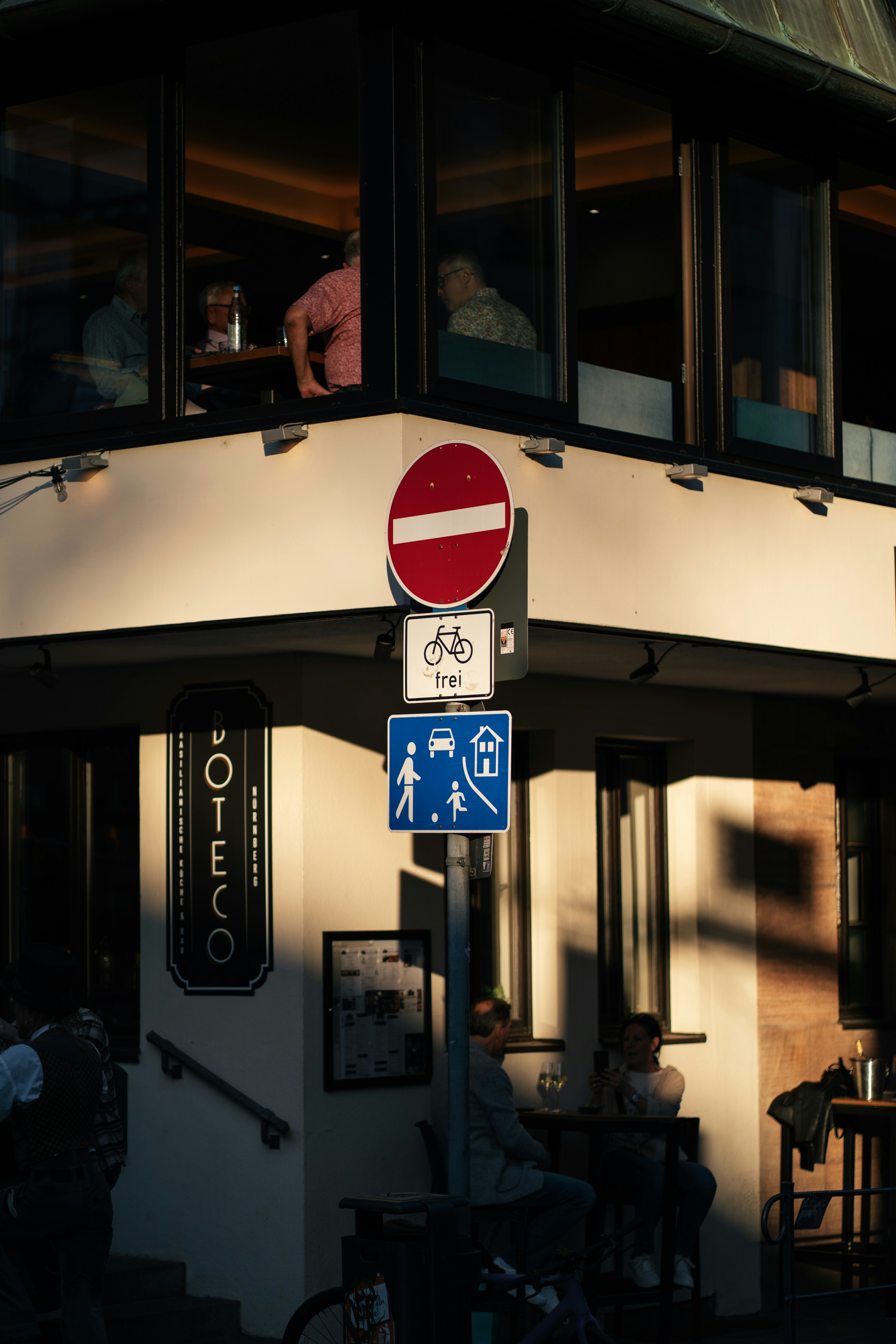 A corner building displays road signs, with people. photo – Free Woman ...