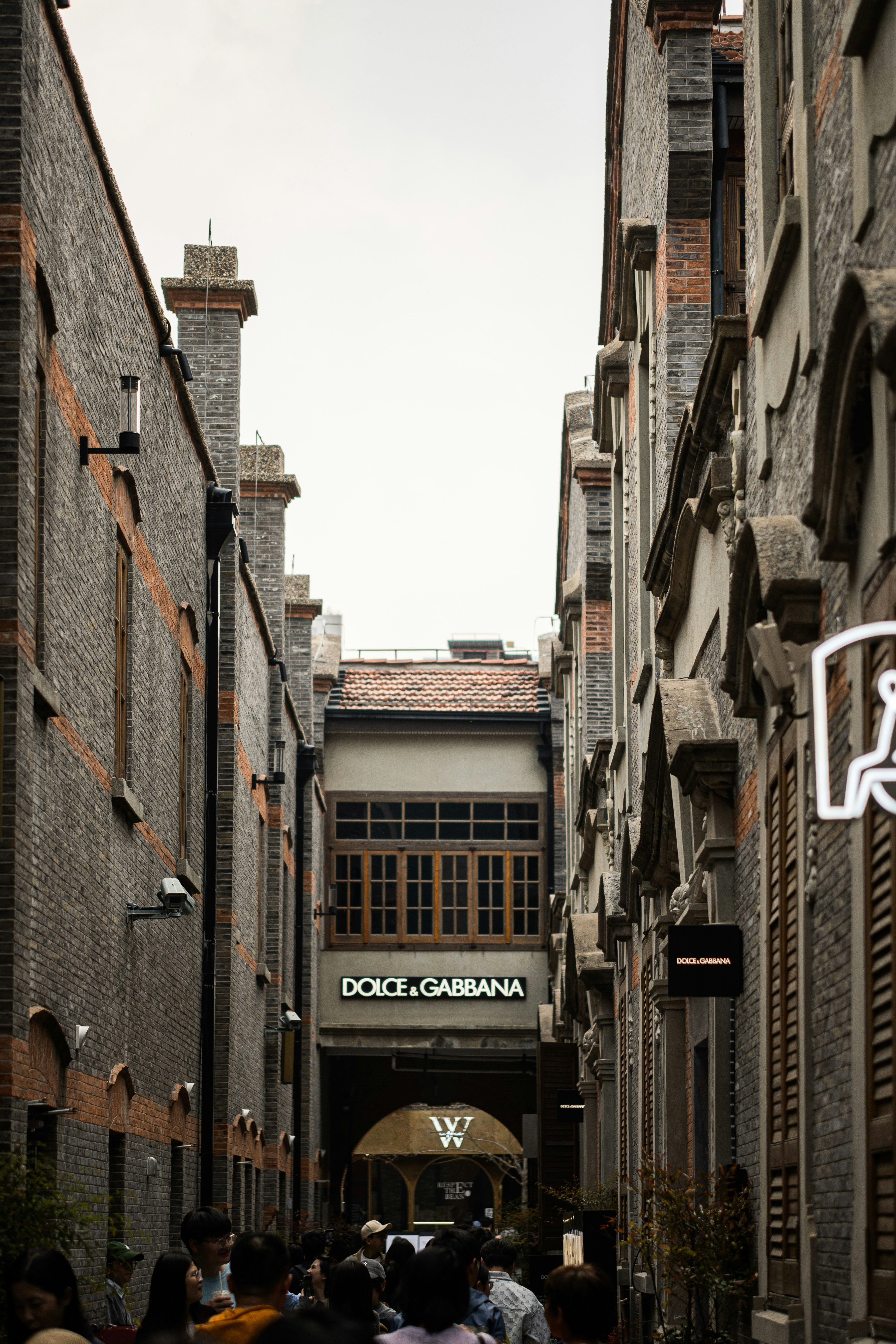 Narrow alley with historic brick buildings leading to a Dolce & Gabbana store entrance under a cloudy sky.