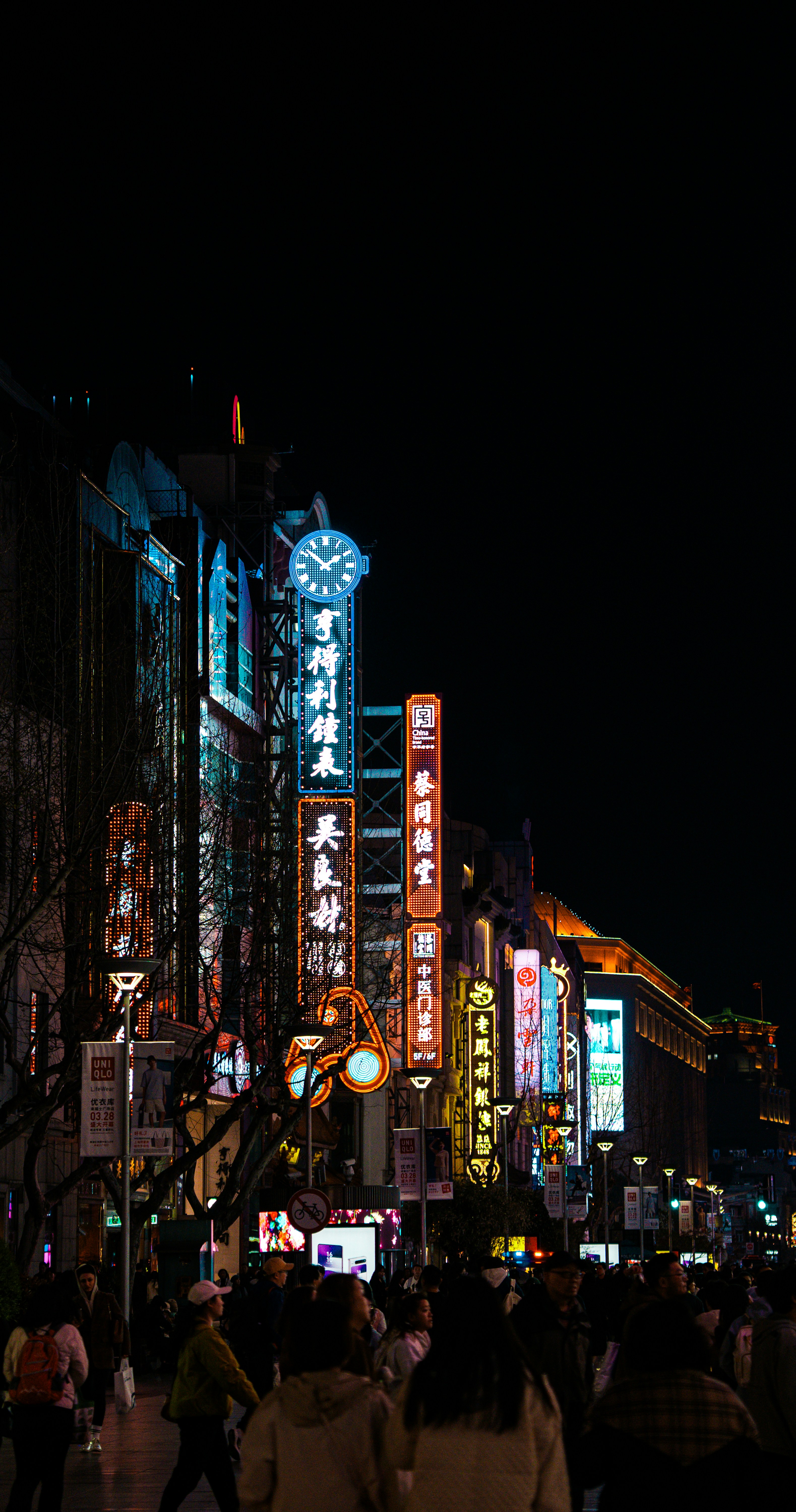 Vibrant neon signs illuminate a bustling city street filled with people at night.
