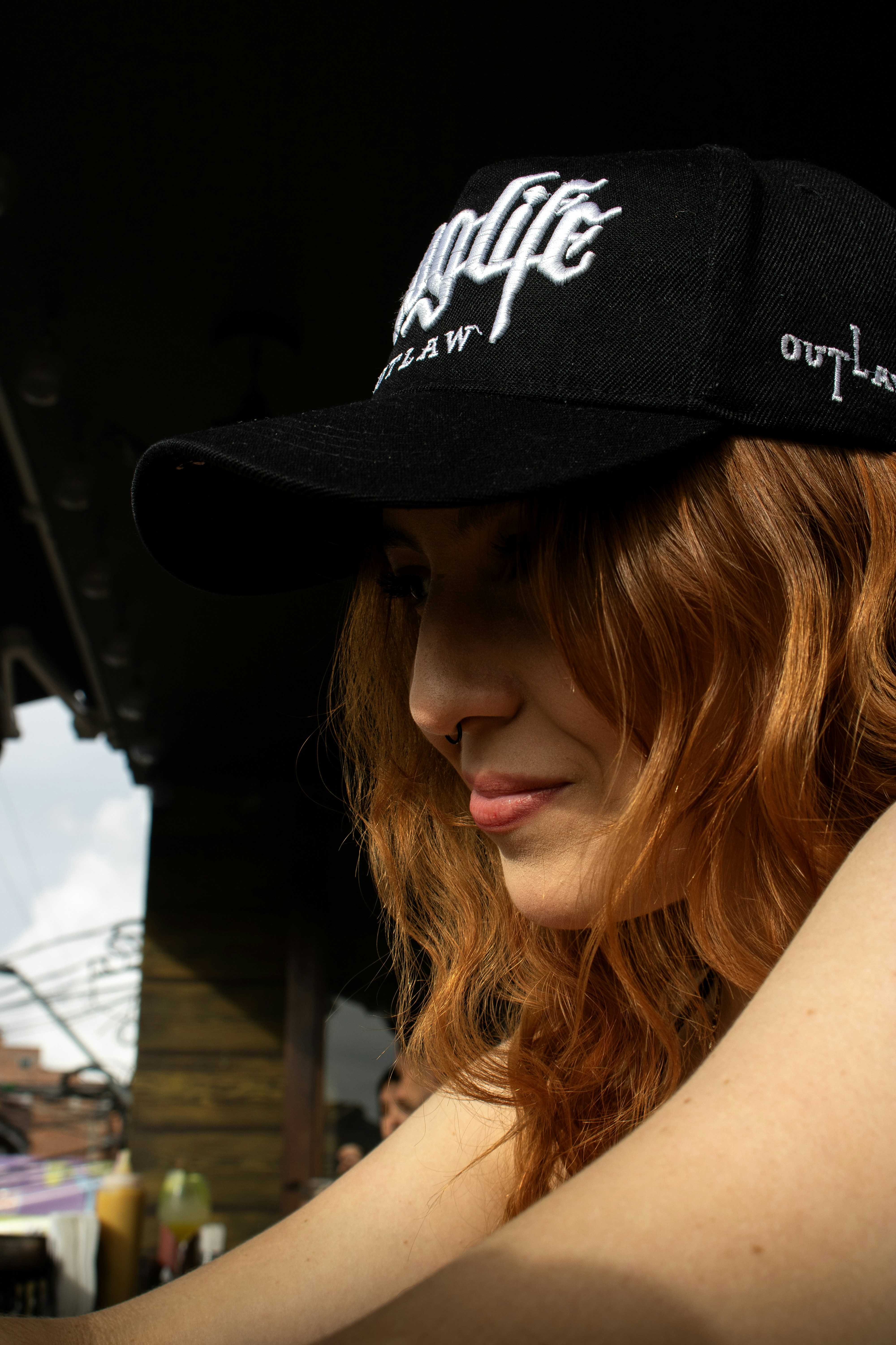 Woman with red hair wearing a black cap, smiling under bright sunlight.