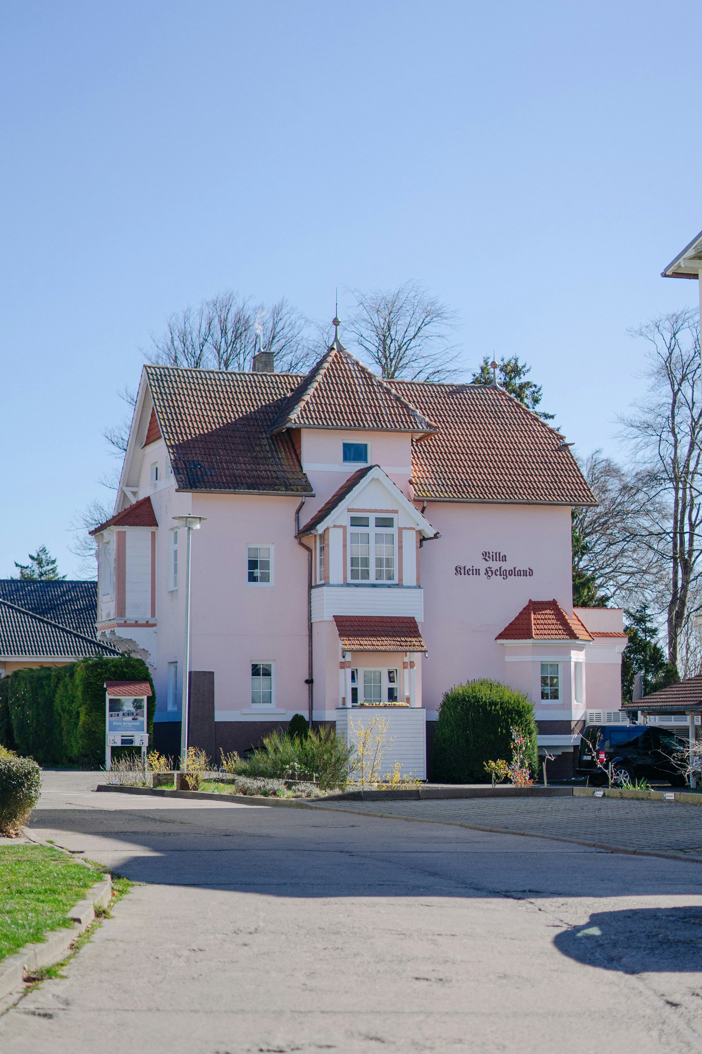 Pink house with intricate architectural details and surrounding greenery under a clear blue sky.
