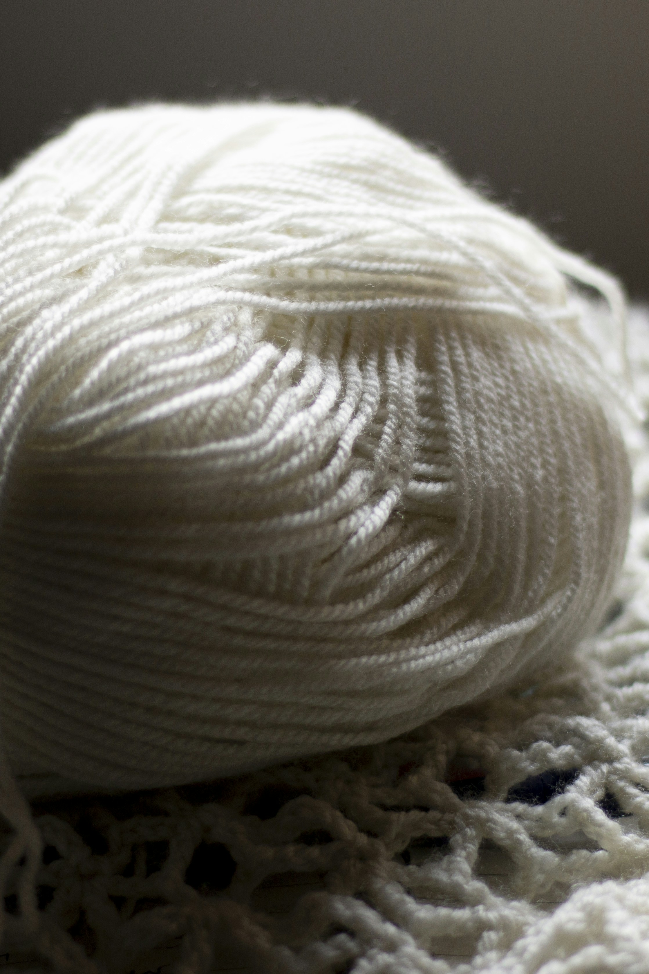 Ball of white yarn resting on a crocheted surface in soft lighting.