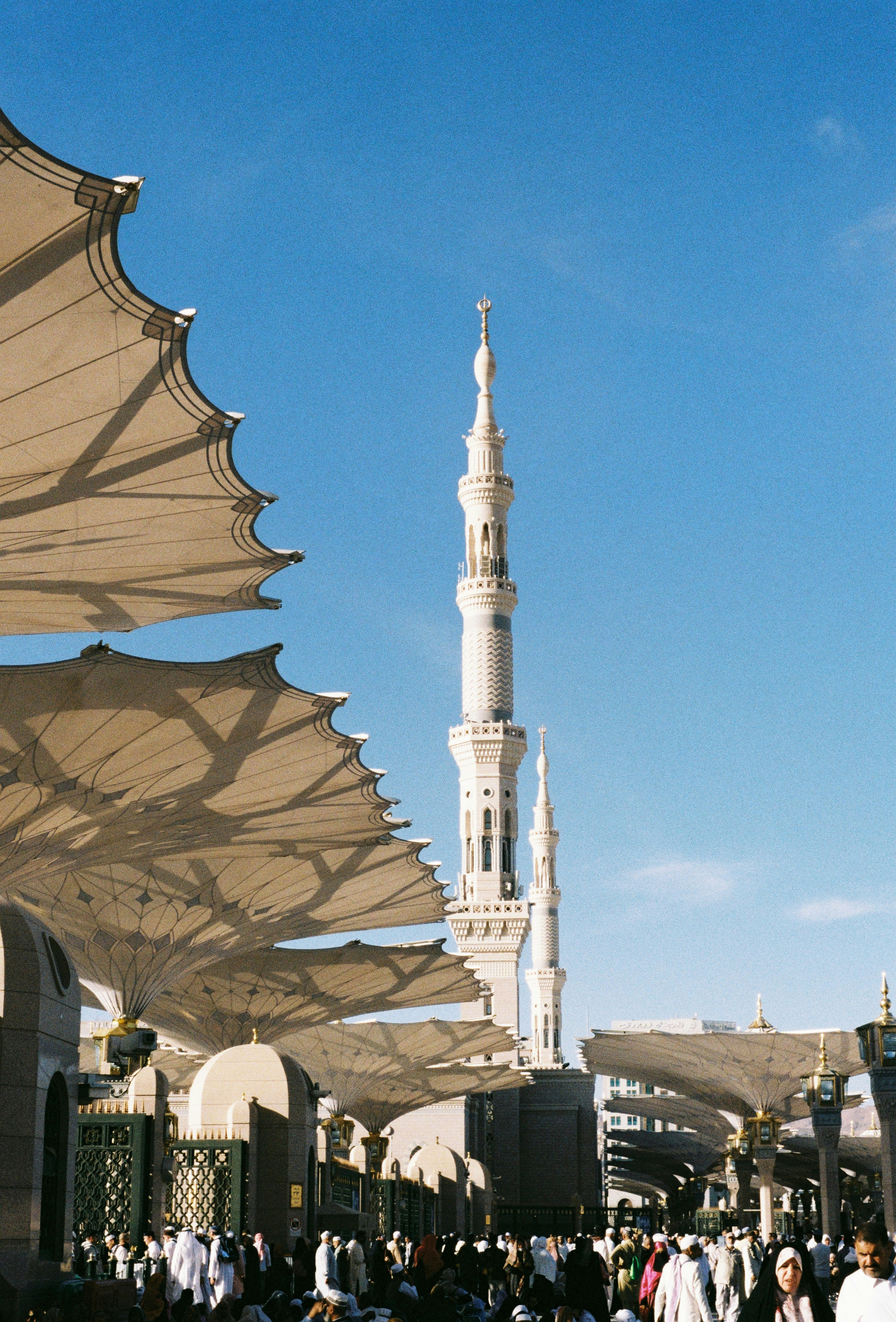 Towering minaret and geometric canopies under a bright blue sky.