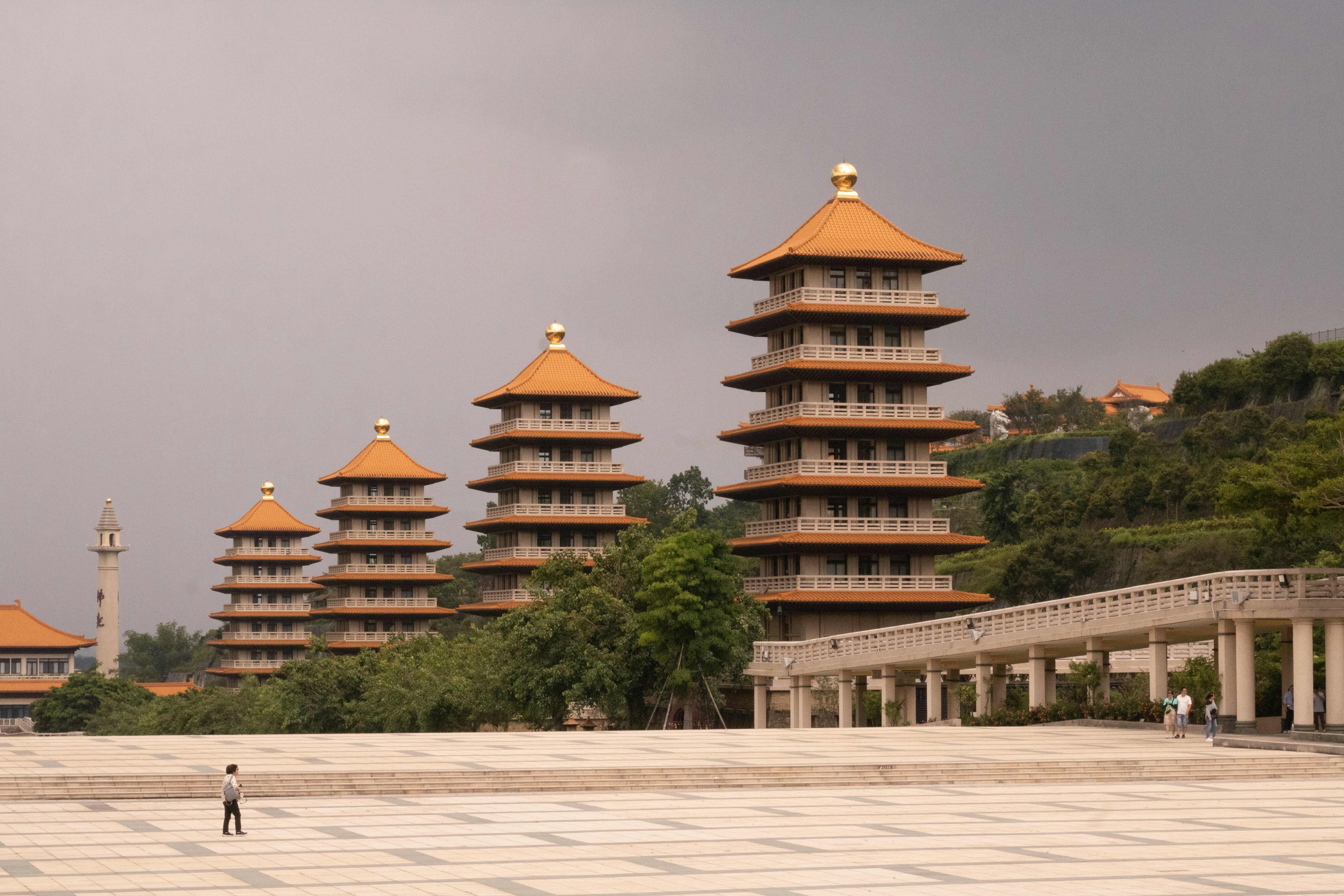 Series of pagodas with orange roofs against a cloudy sky, surrounded by lush greenery.