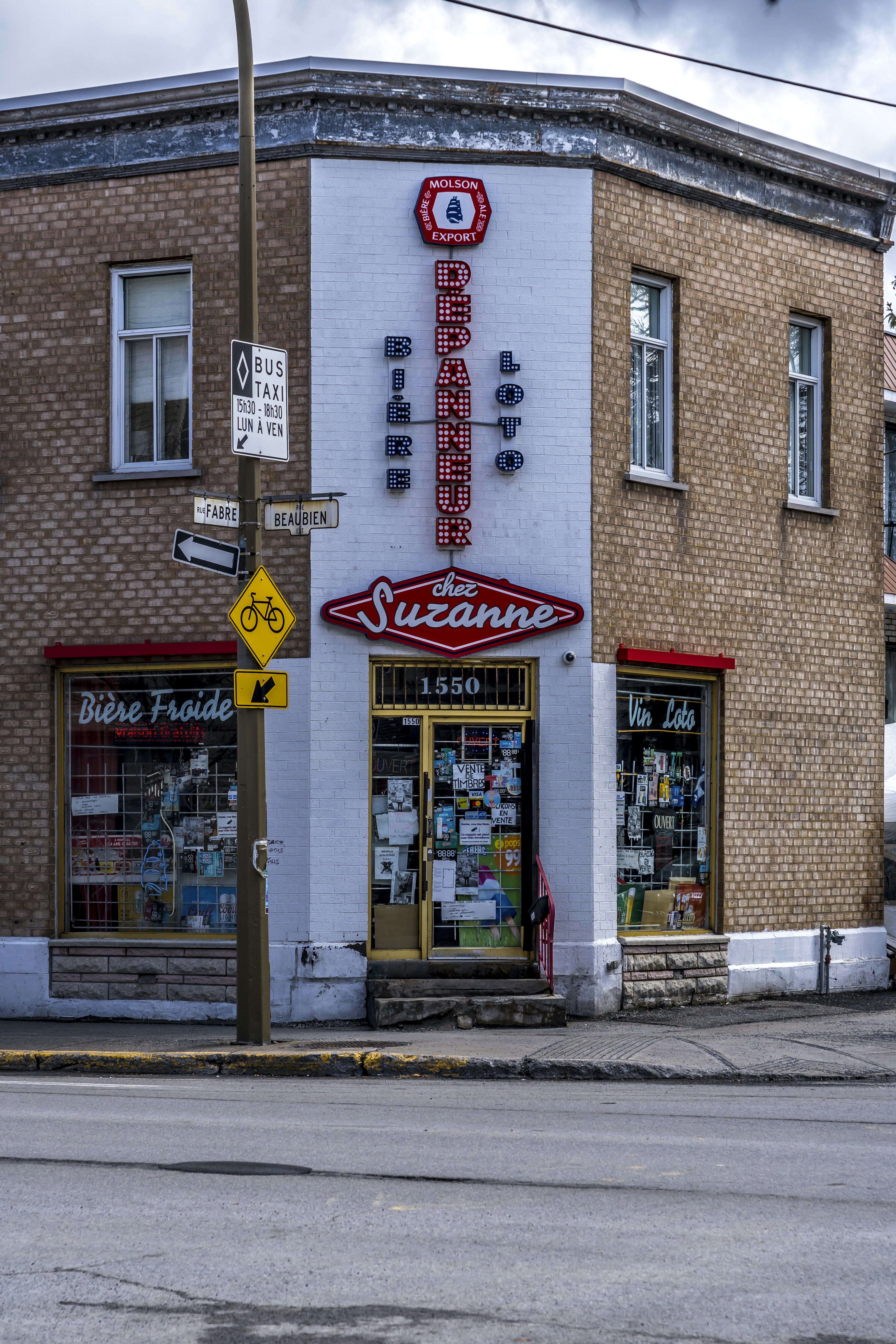 Historic brick corner store with retro signage and colorful window displays under a cloudy sky.