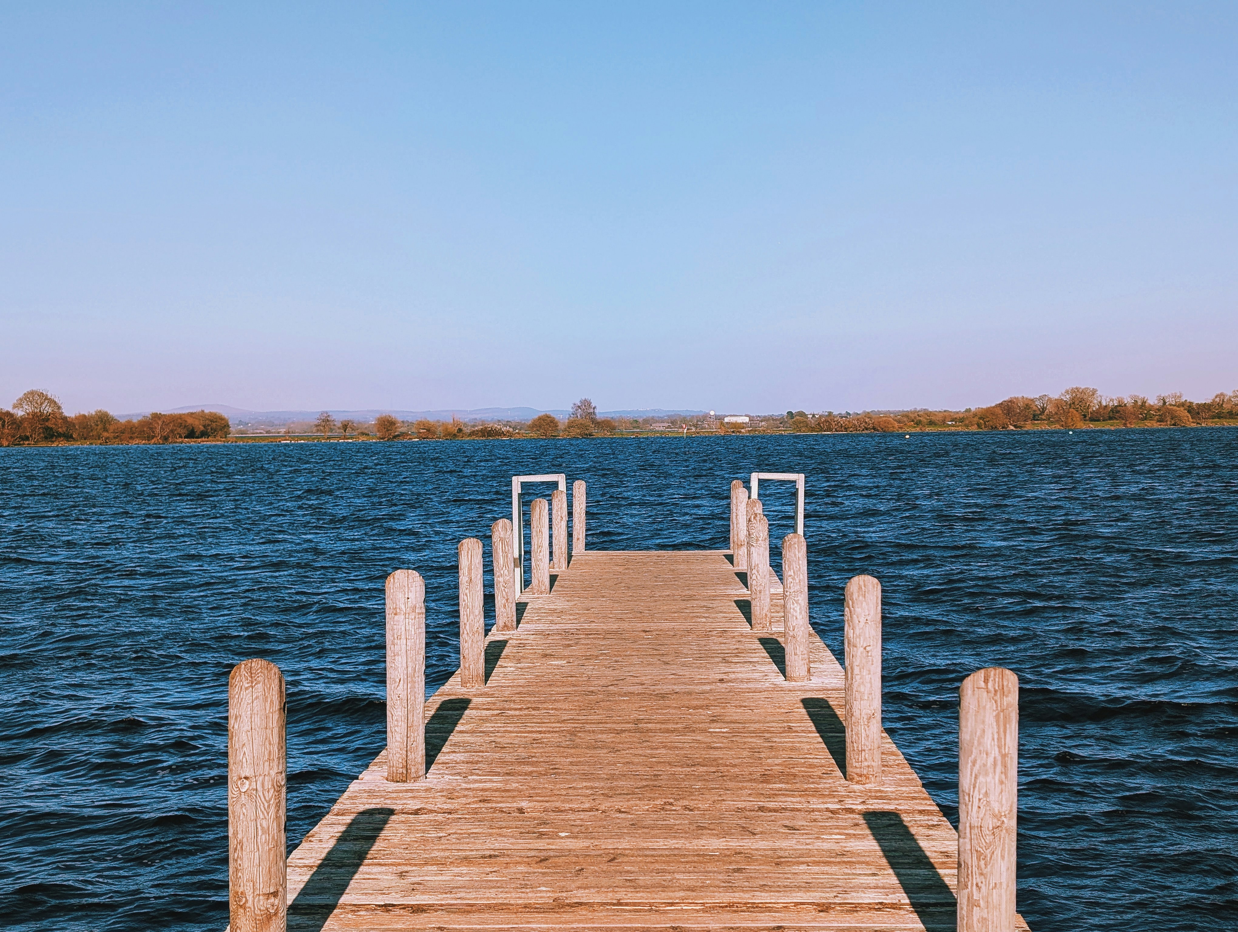 Wooden pier extending into the calm waters of Lough Neagh under a clear blue sky.