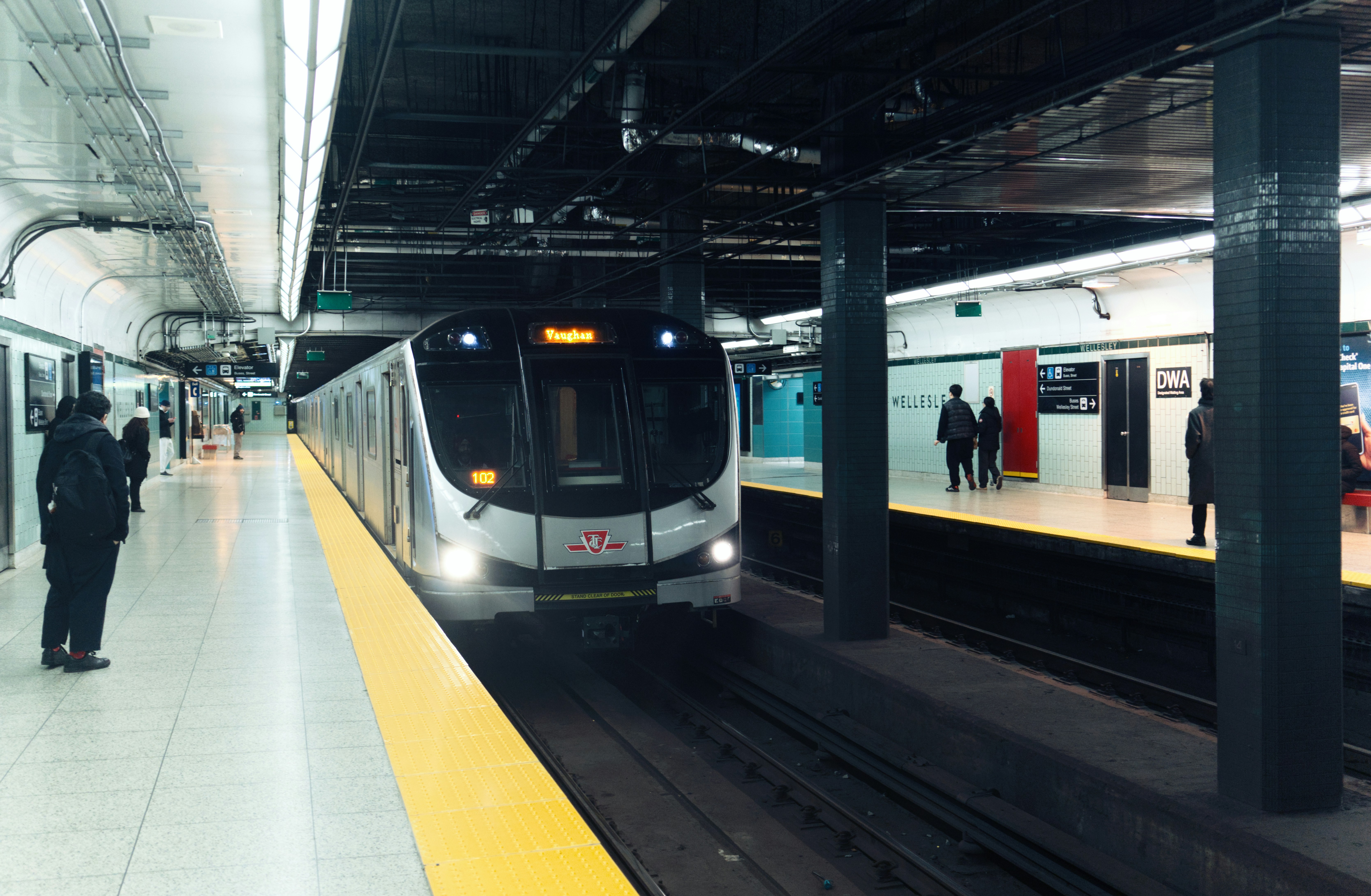 Subway train approaching a platform in a brightly lit underground station with waiting passengers.