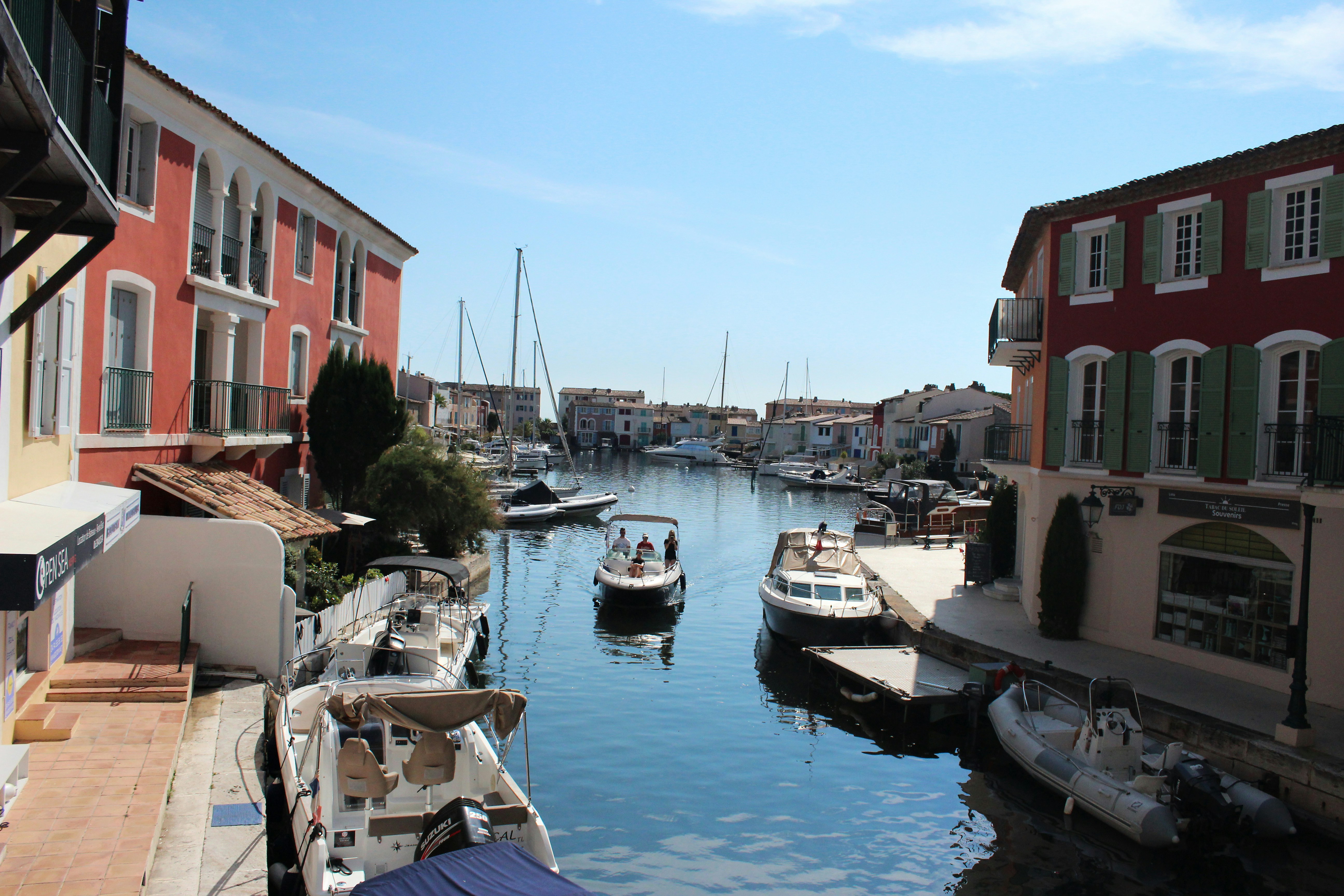 Boats moored along a tranquil canal flanked by colorful buildings under a bright blue sky.