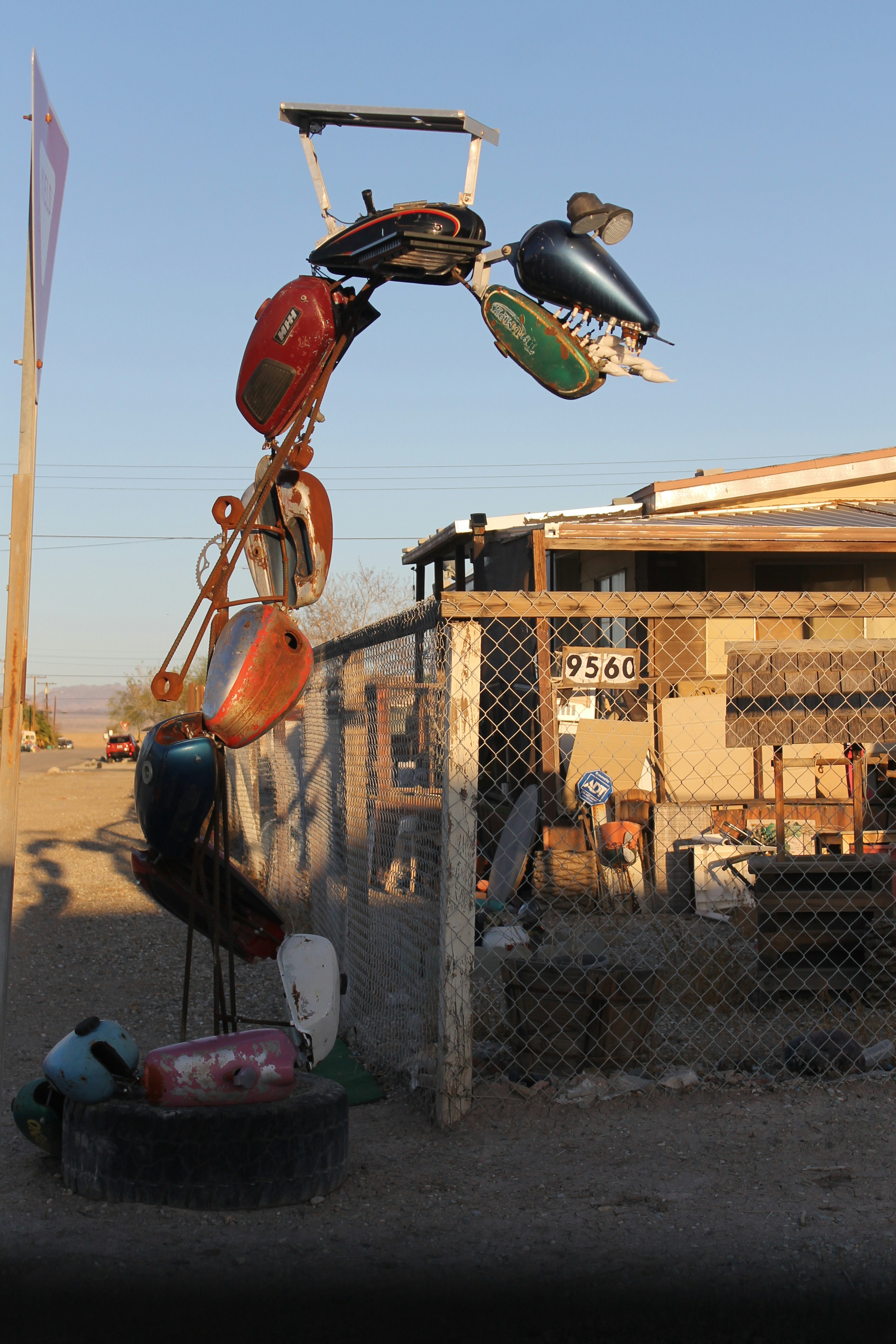 Desert Junkyard Totem: A Colorful Car-Seat Sculpture Rising Over a Chain-Link Yard