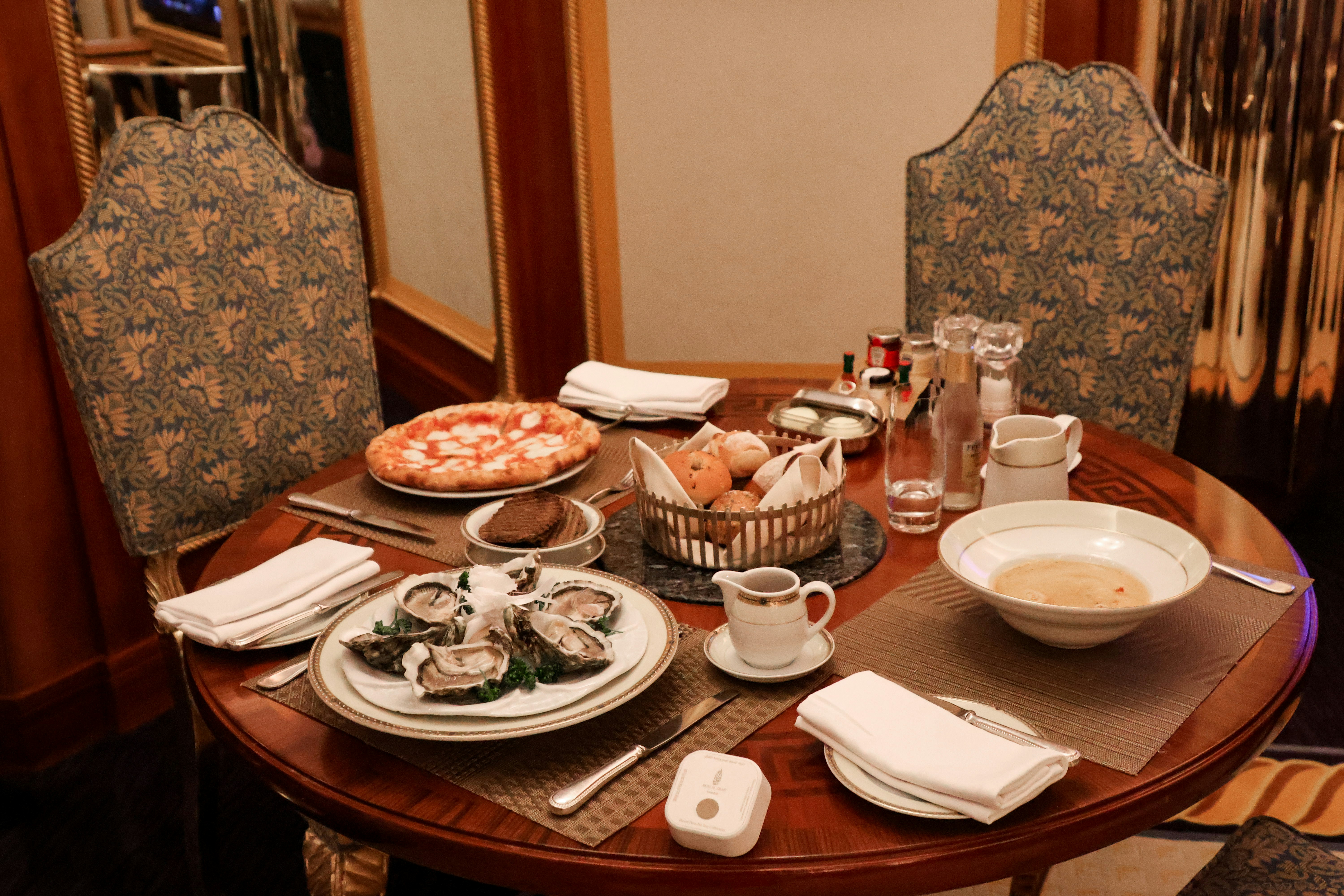 An elegantly set dining table featuring oysters, a pizza, and various accompaniments, showcasing a luxurious dining experience.