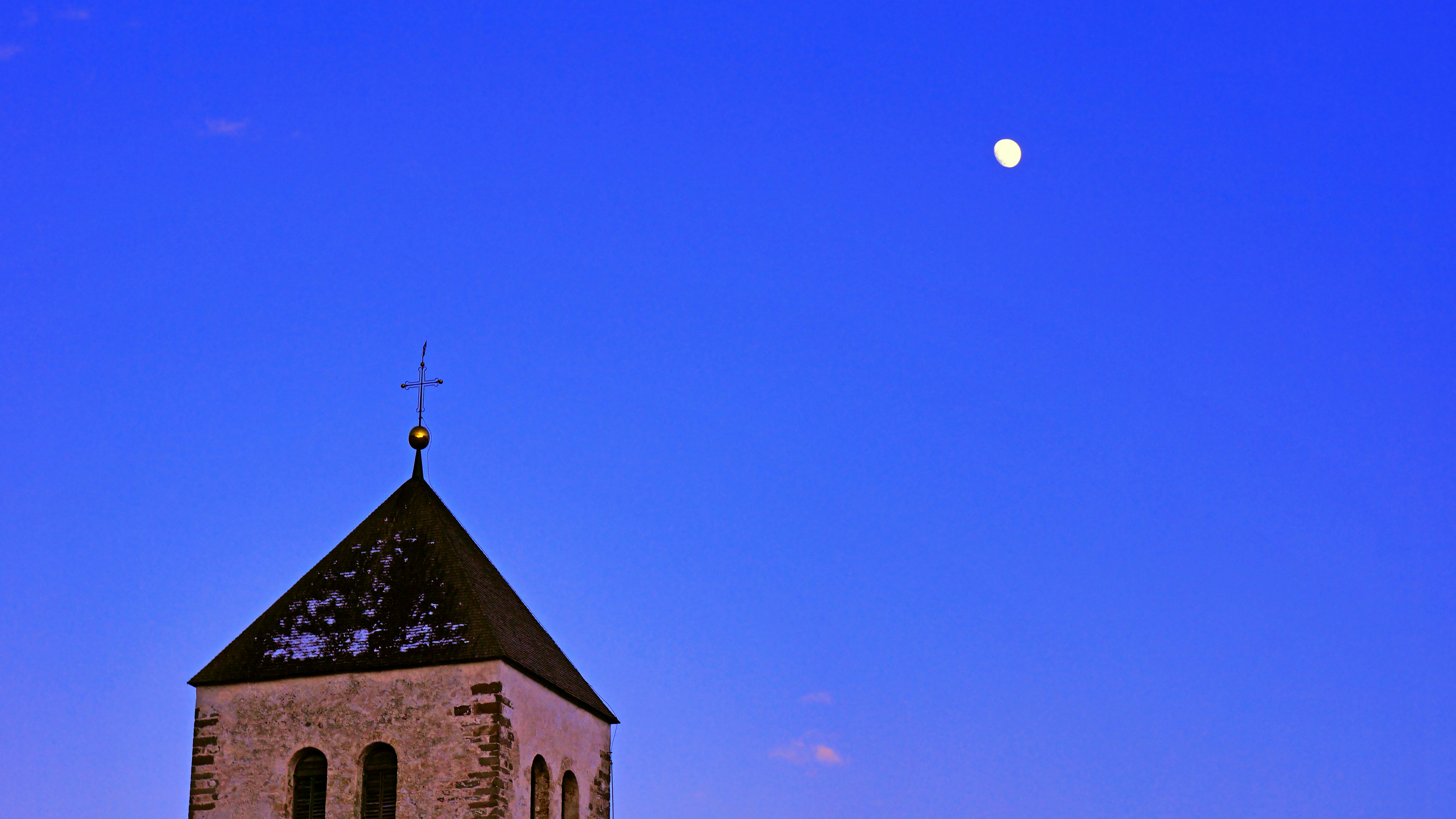 Stone tower with a steep roof under a twilight sky featuring a bright moon.