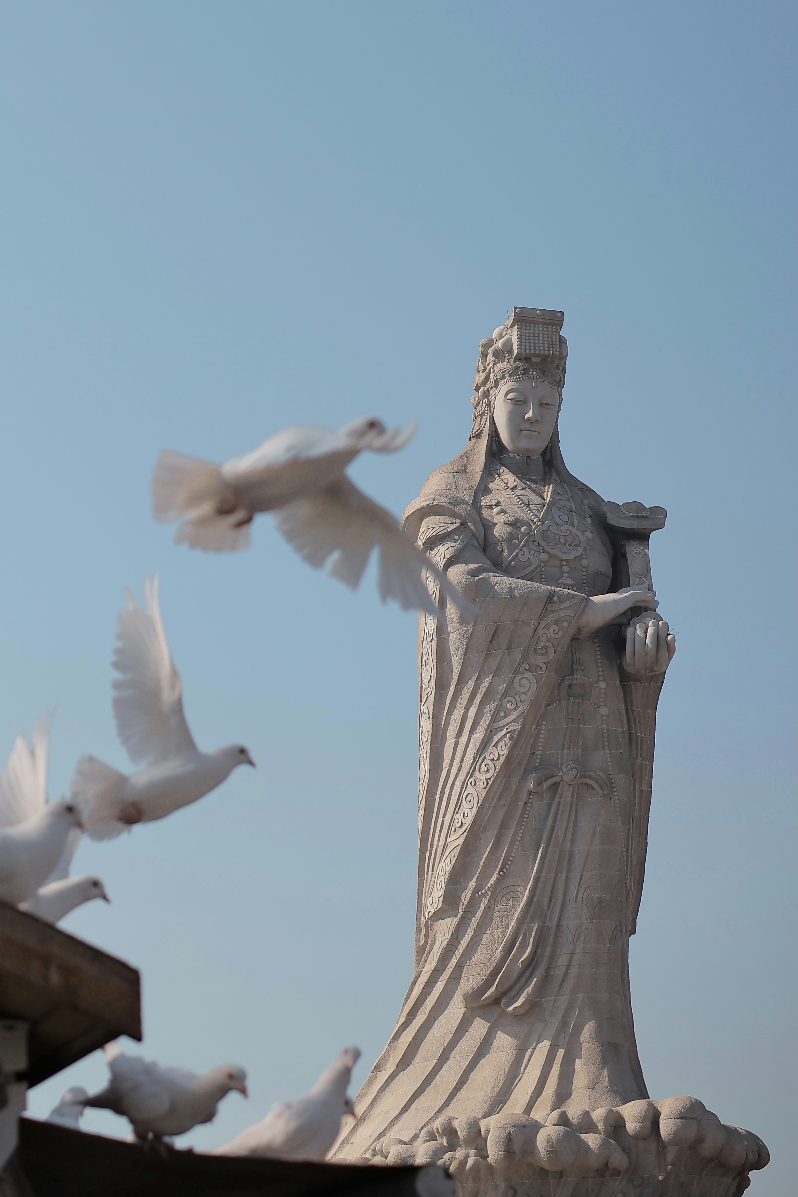 Stone Guanyin Amid Doves Under a Cerulean Sky