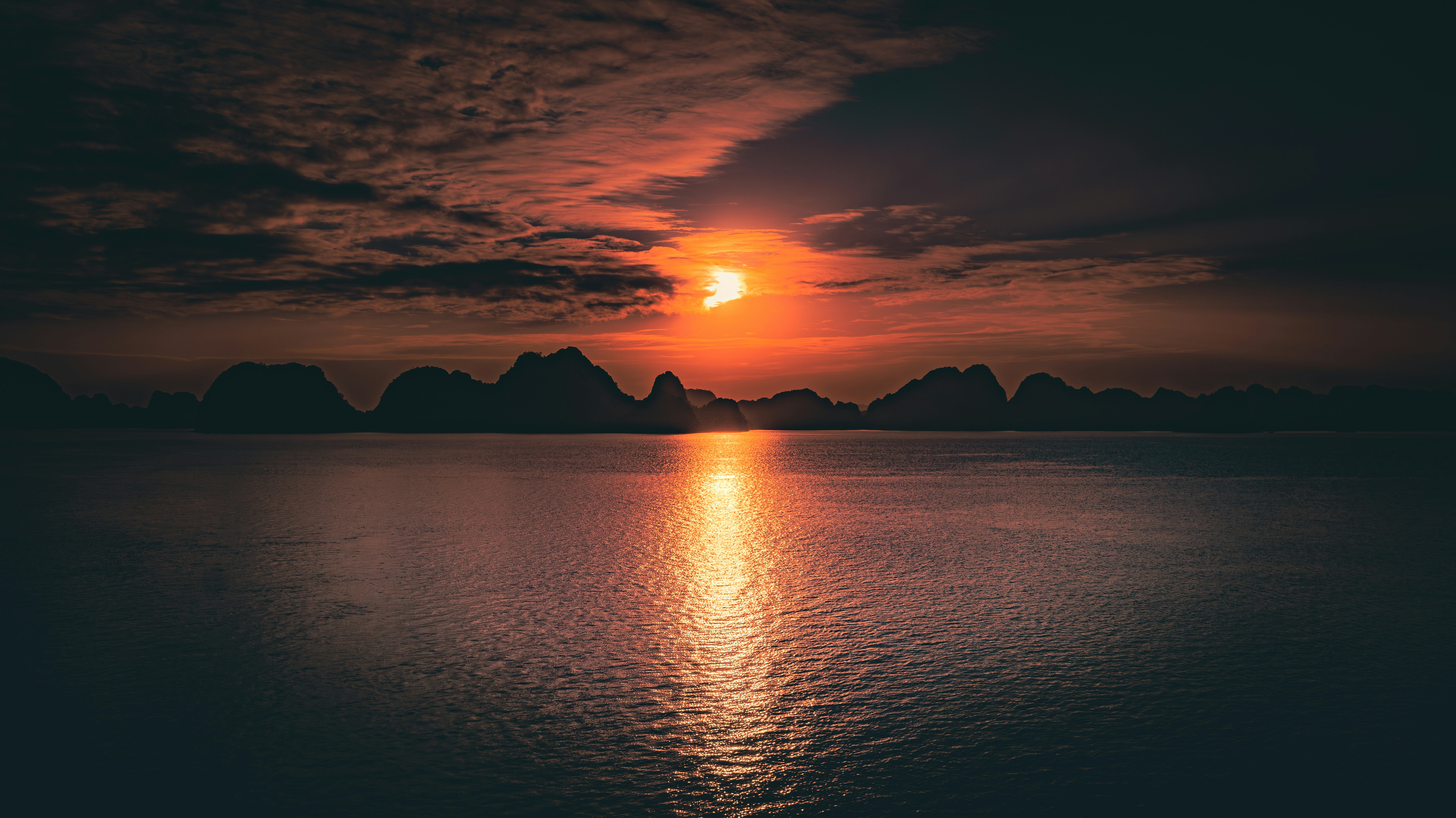 Sunset over a calm sea with silhouetted mountains on the horizon.
