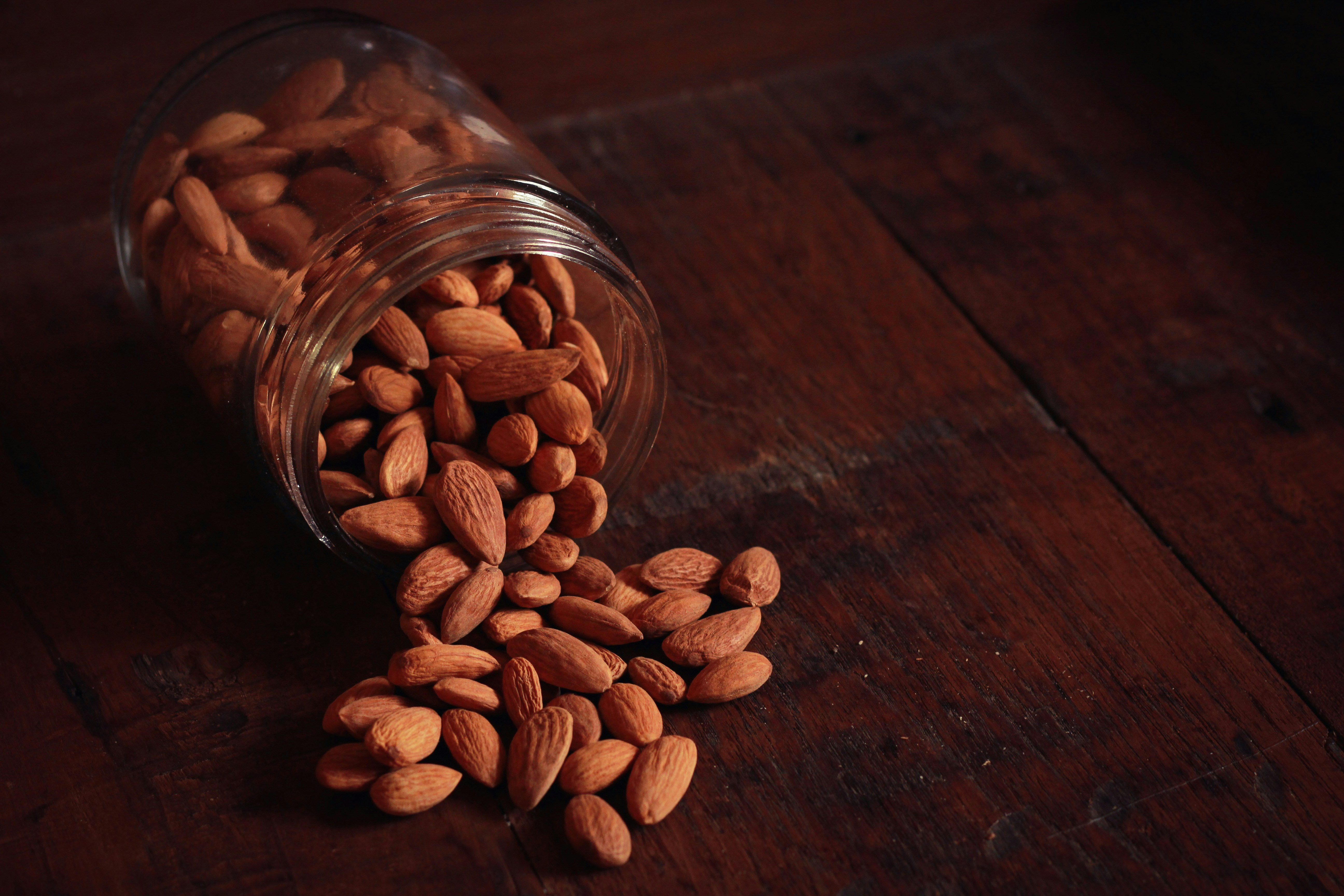 Scattered almonds spilling from a glass jar onto a wooden surface, highlighting their natural texture and color.