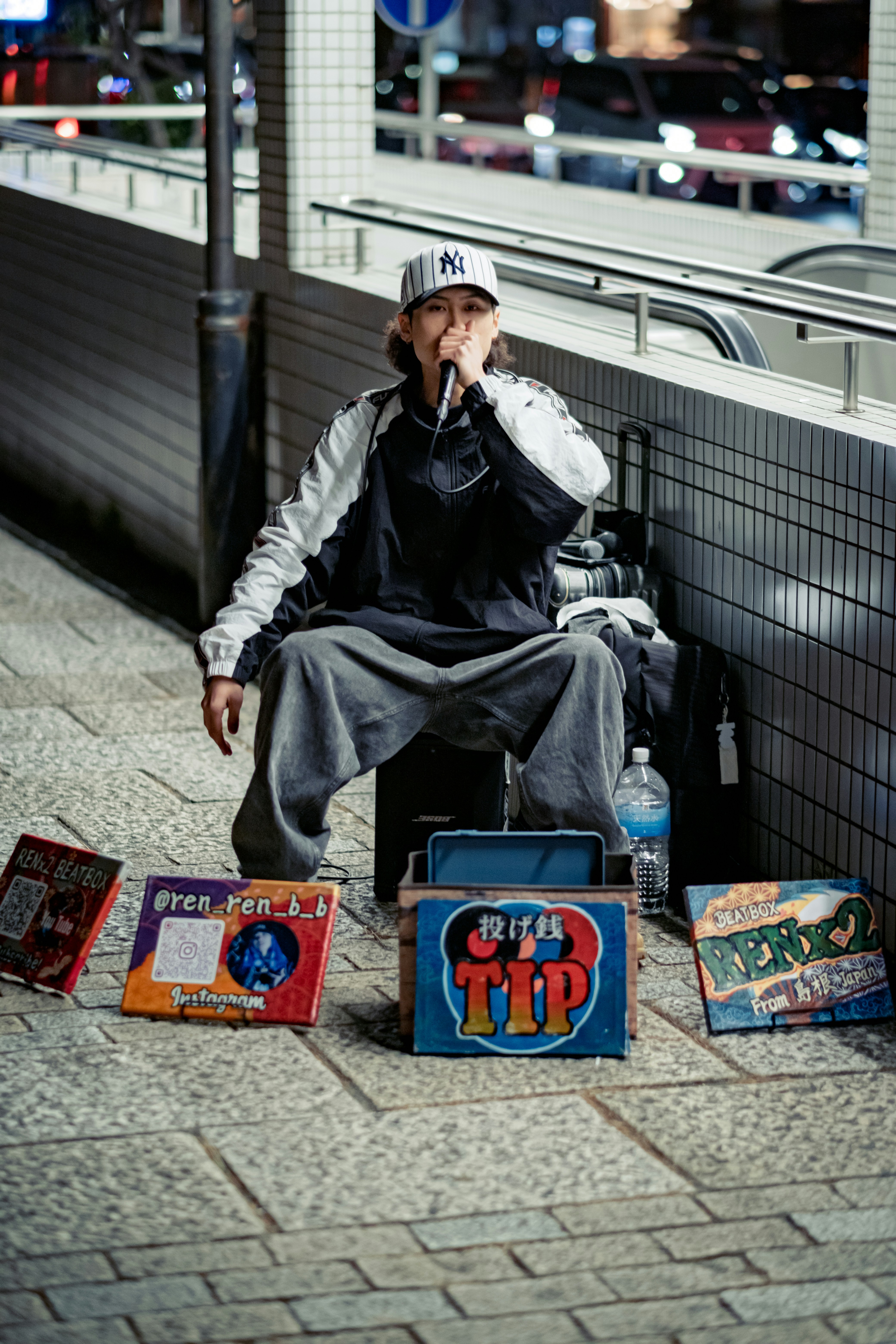 Street performer with microphone surrounded by colorful music-themed boxes on a tiled walkway.
