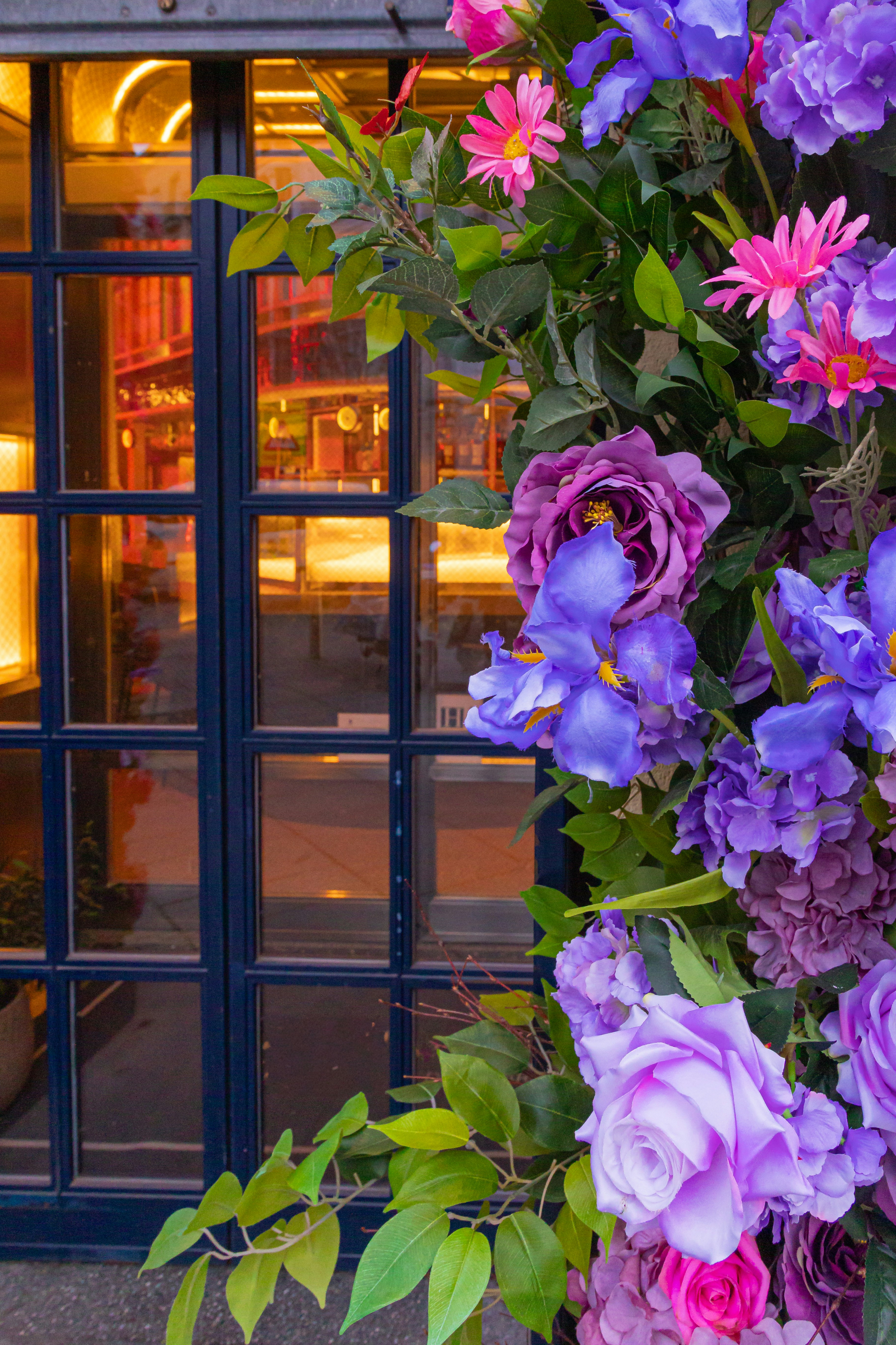 Colorful arrangement of pink and purple flowers against a glass-paned door reflecting urban lights.