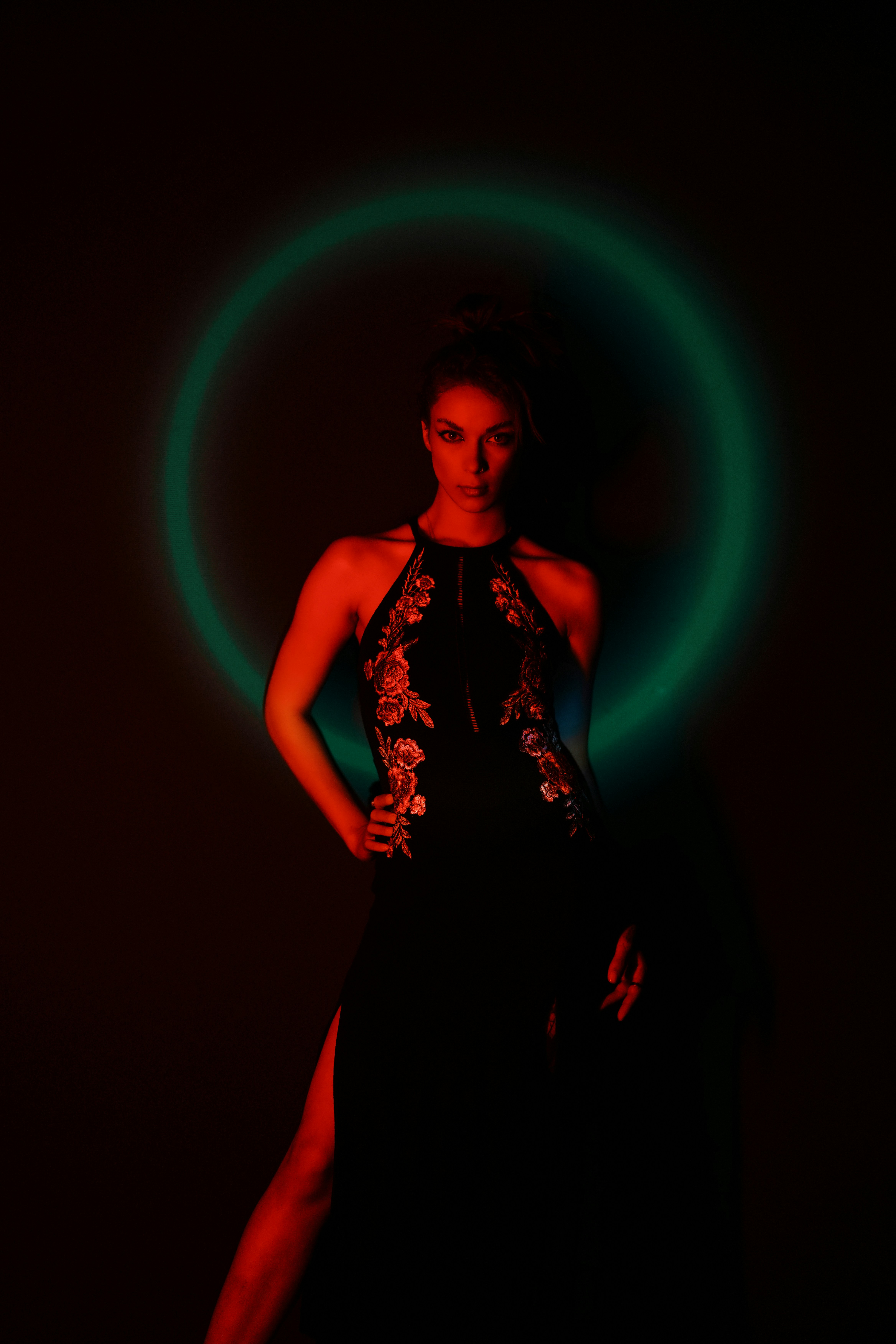 Person in an ornate dress stands against a dark backdrop, framed by a glowing circular light.