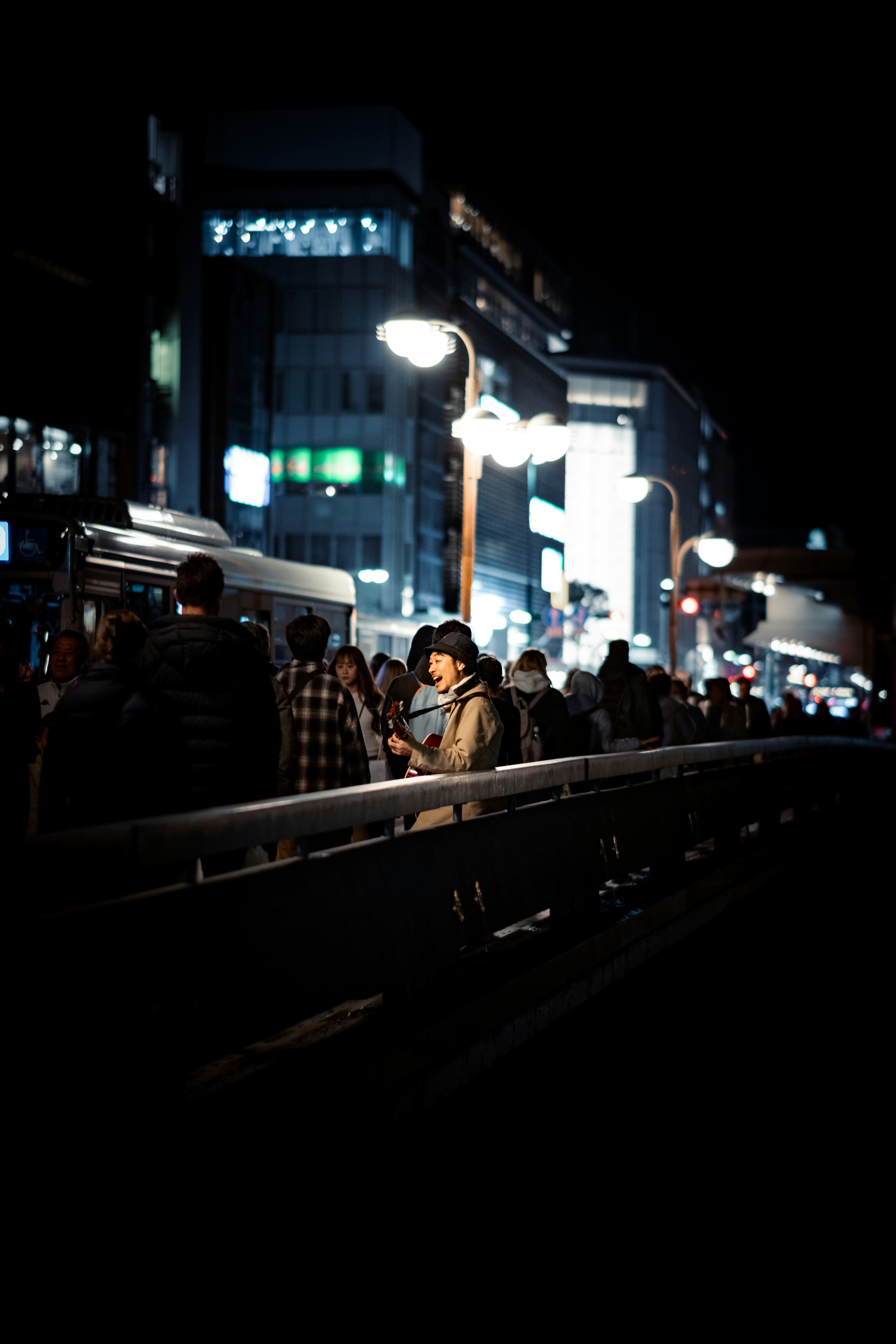 Person in a bustling city street illuminated by streetlights and distant neon signs at night.