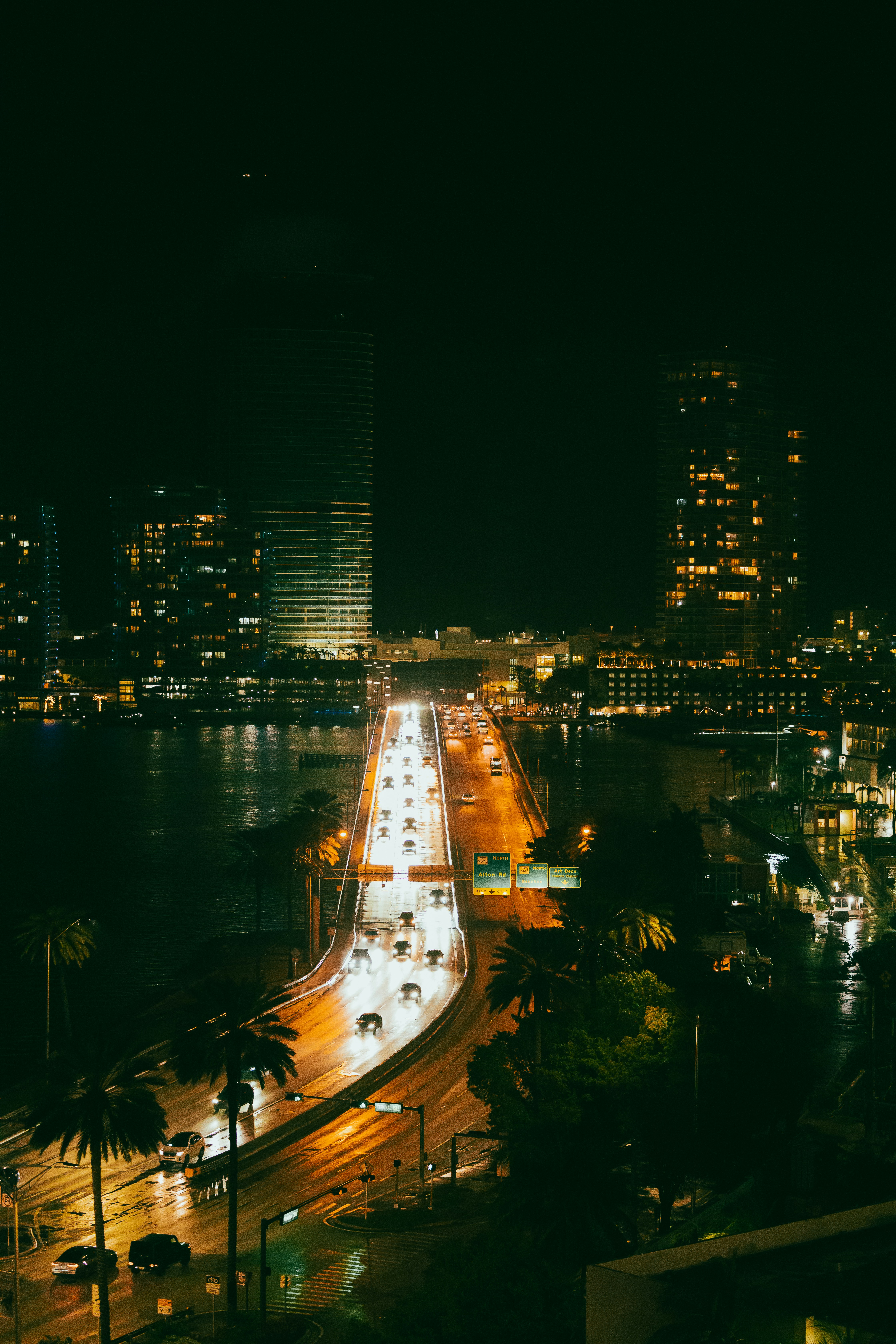 City lights reflecting on MacArthur Causeway with a stream of car headlights under a dark sky.