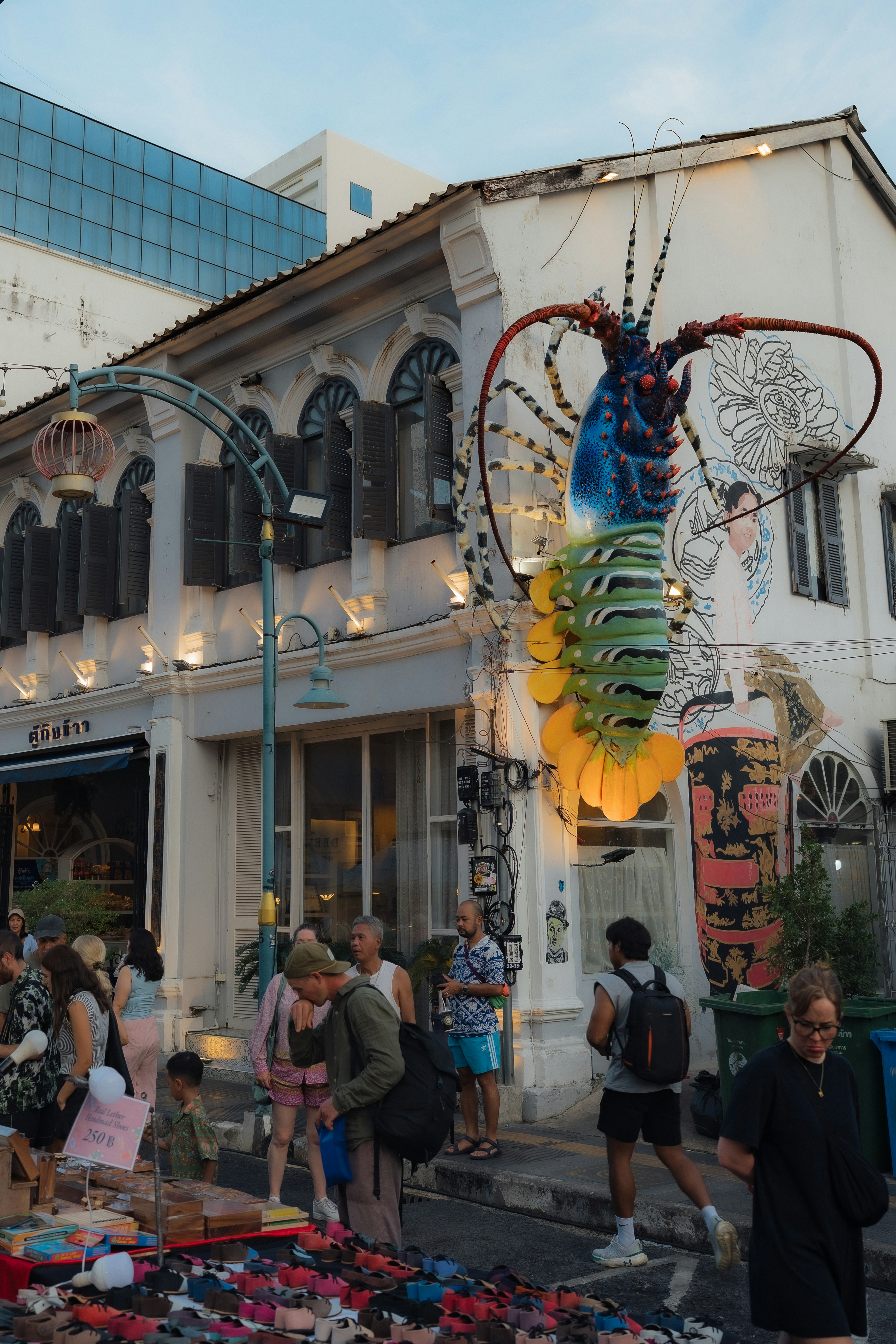 Crowd gathers at a bustling night market in Phuket Old Town, with colorful street art and vibrant market stalls.