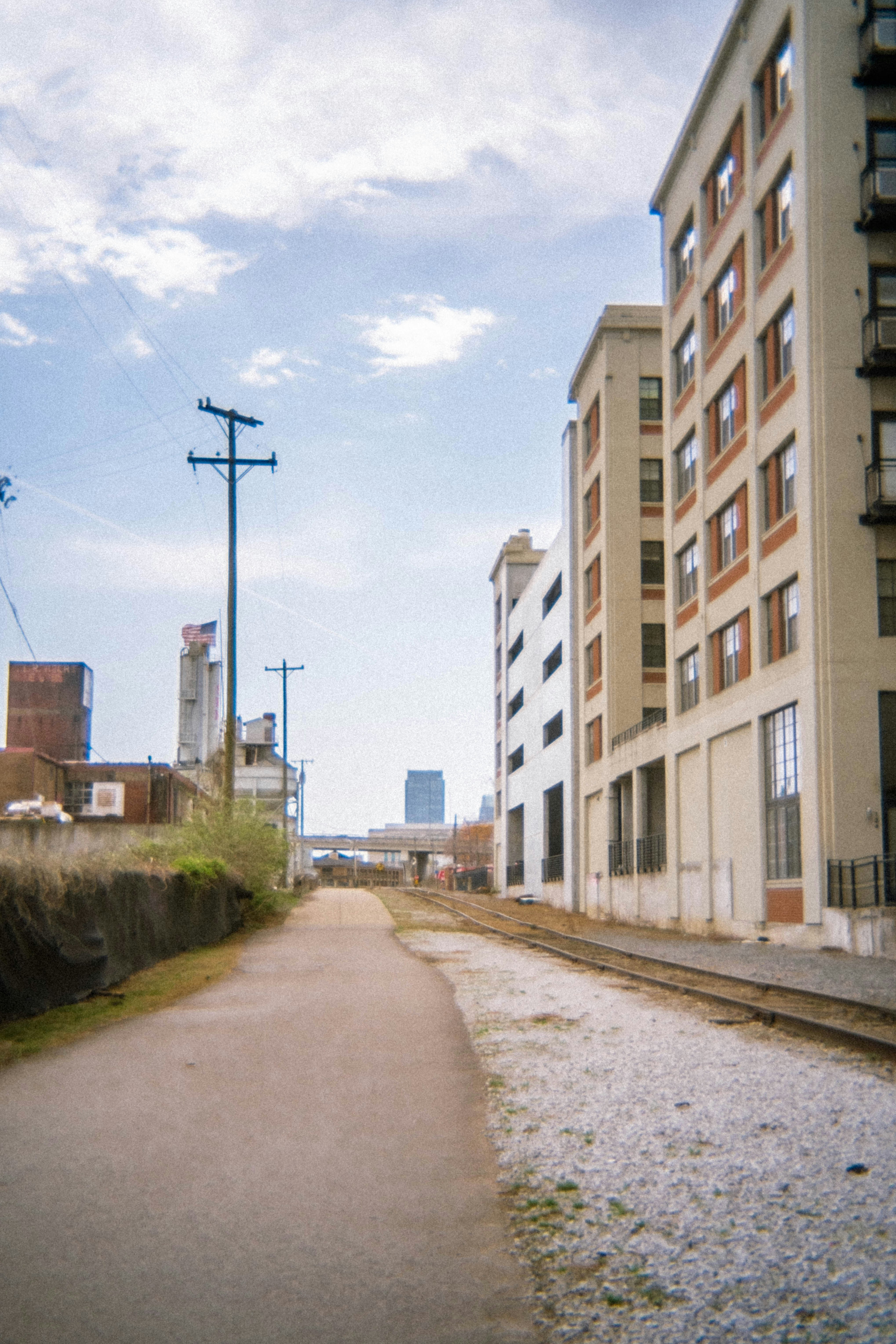Empty alleyway flanked by industrial buildings and train tracks under a bright blue sky.