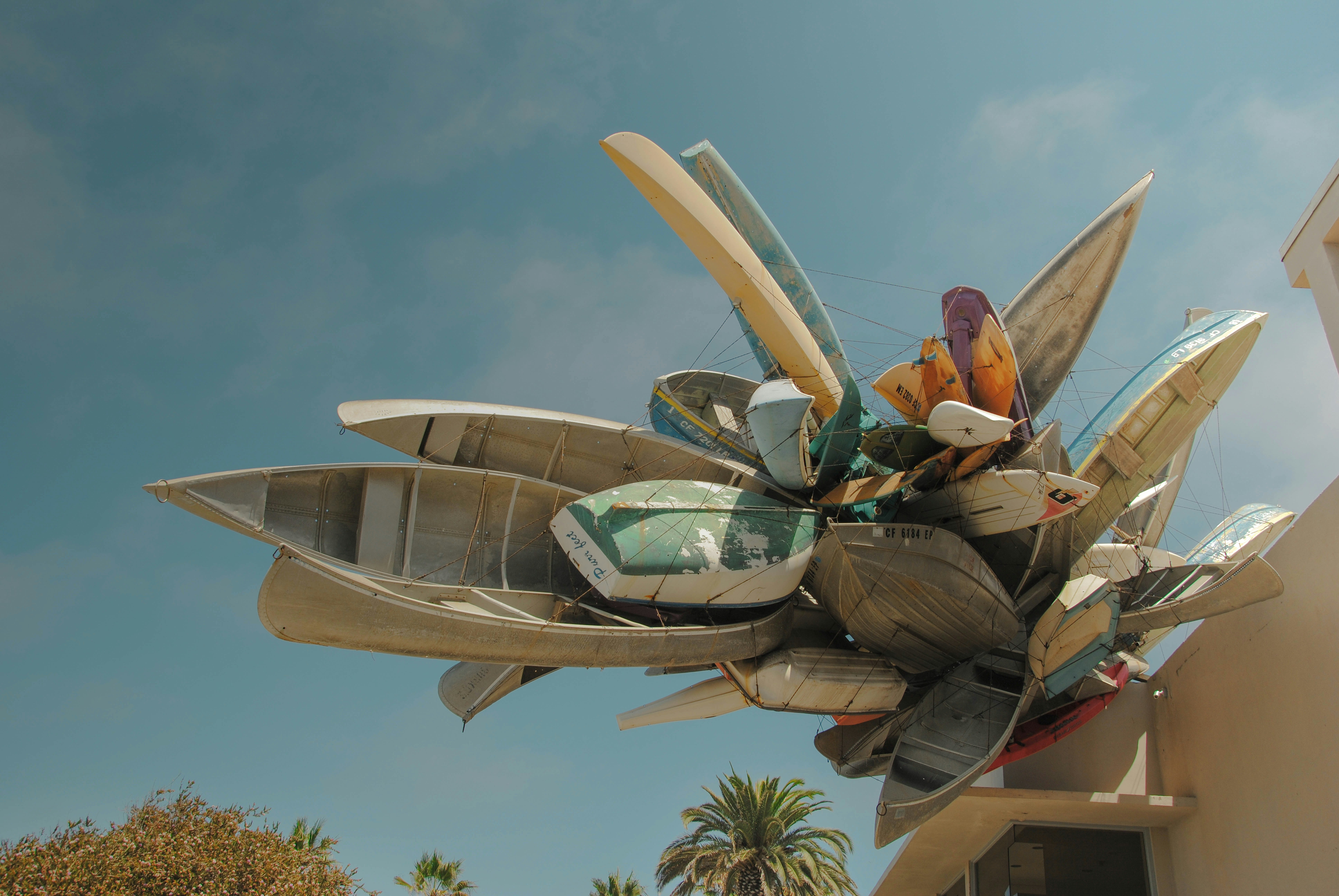 Sculpture of intertwined boats jutting into a clear sky with palm trees in the background.