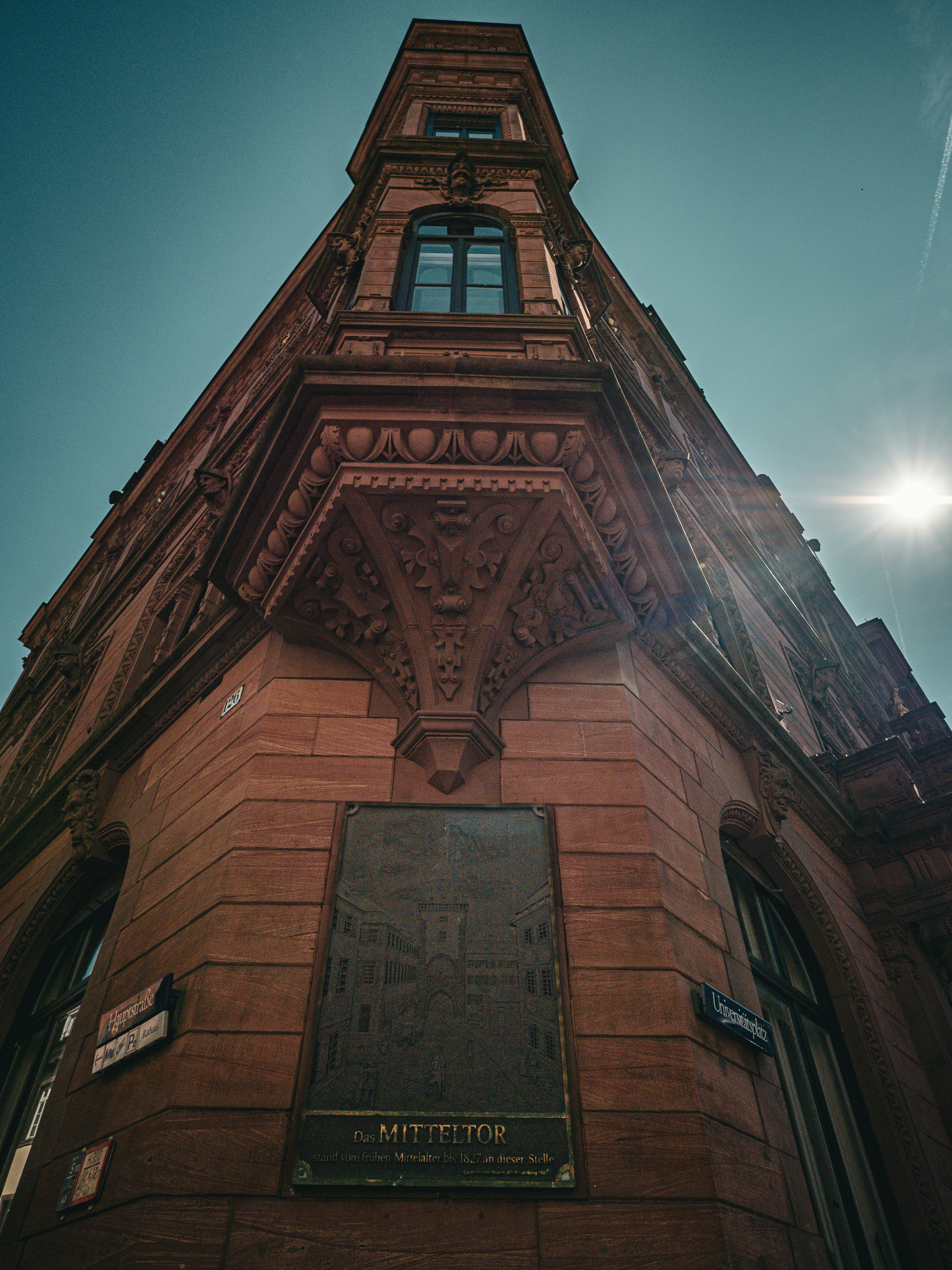 Upward view of a historic brick building corner with ornate details against a bright blue sky.