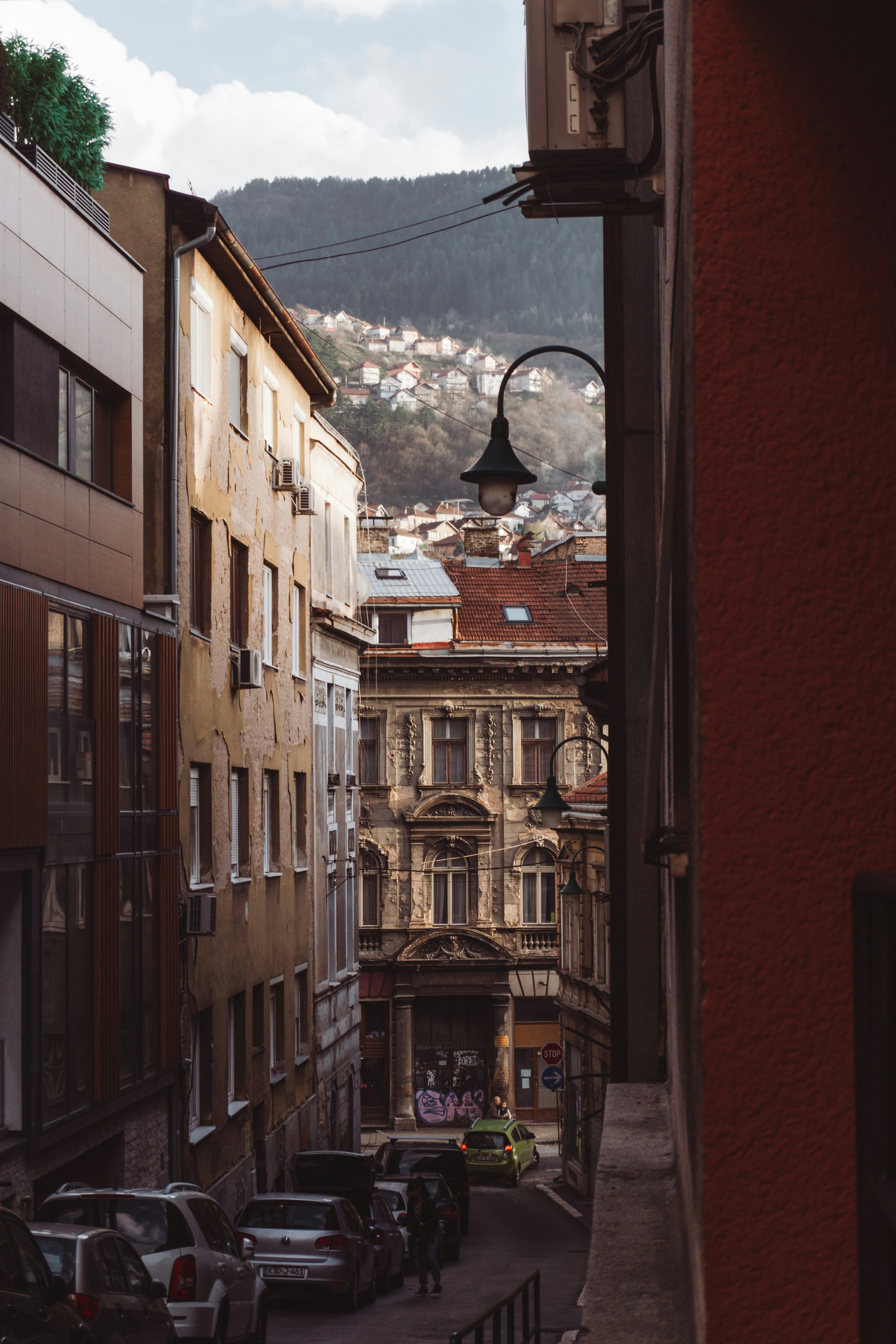 Historic architecture peeks through a narrow urban alley, framed by contemporary buildings and a distant hillside. The scene captures the blend of old and new.